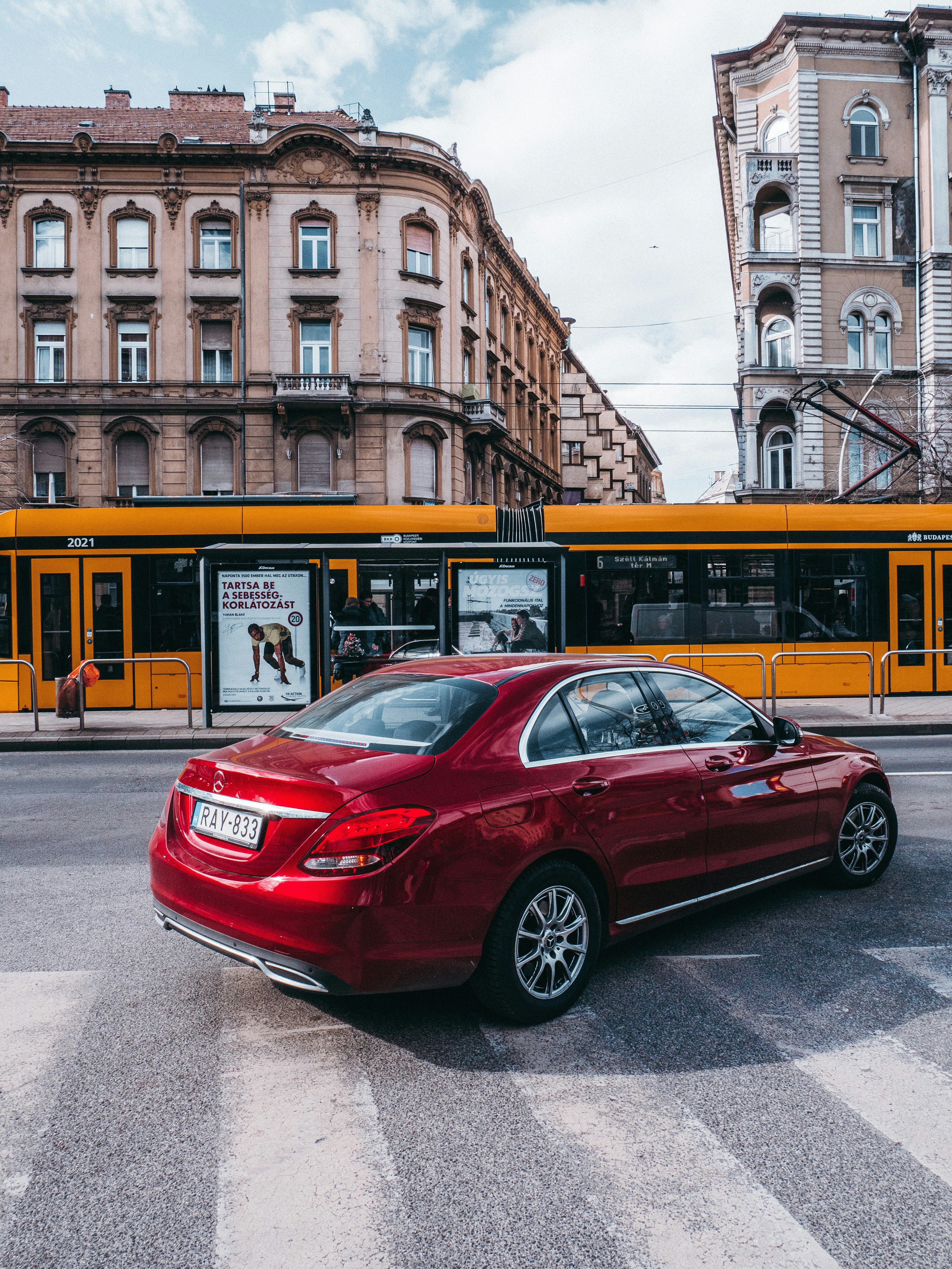 Red Coupe at a City Crossing with a Yellow Tram Backdrop
