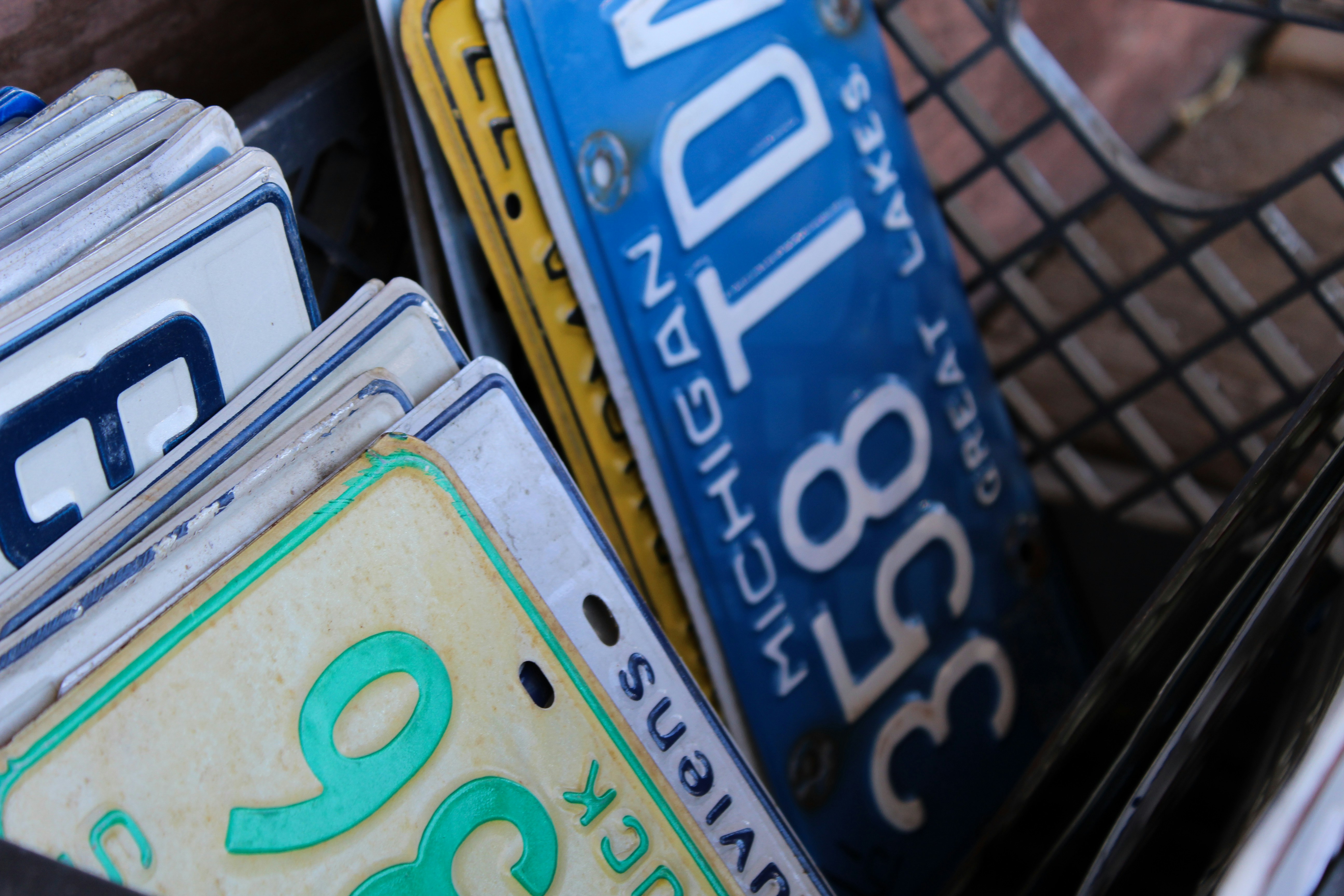 A collection of vintage license plates, showcasing various states and numbers, arranged in a wire basket. The worn textures and colors evoke a sense of nostalgia.