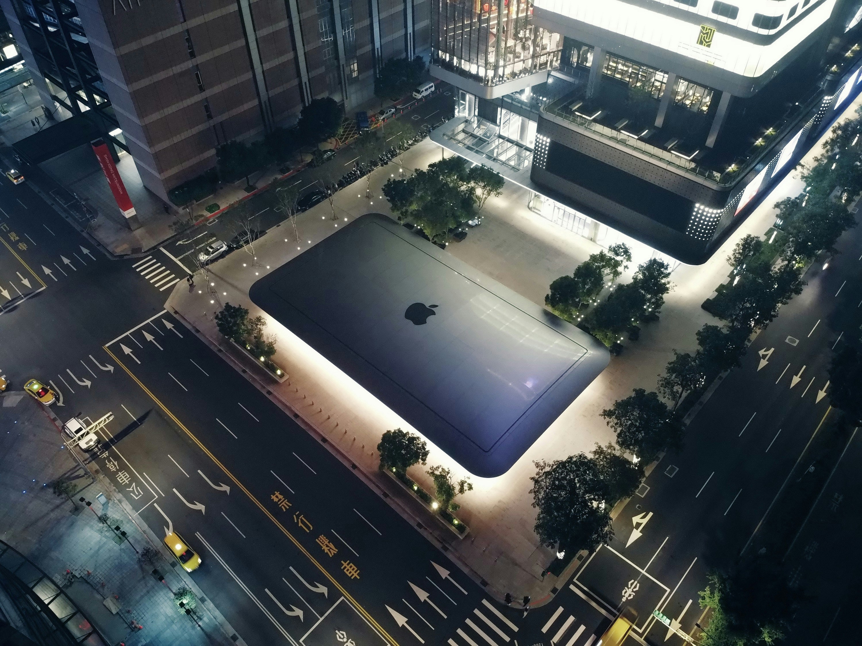 Aerial view of the Apple Pavilion illuminated at night, surrounded by urban greenery and bustling streets.