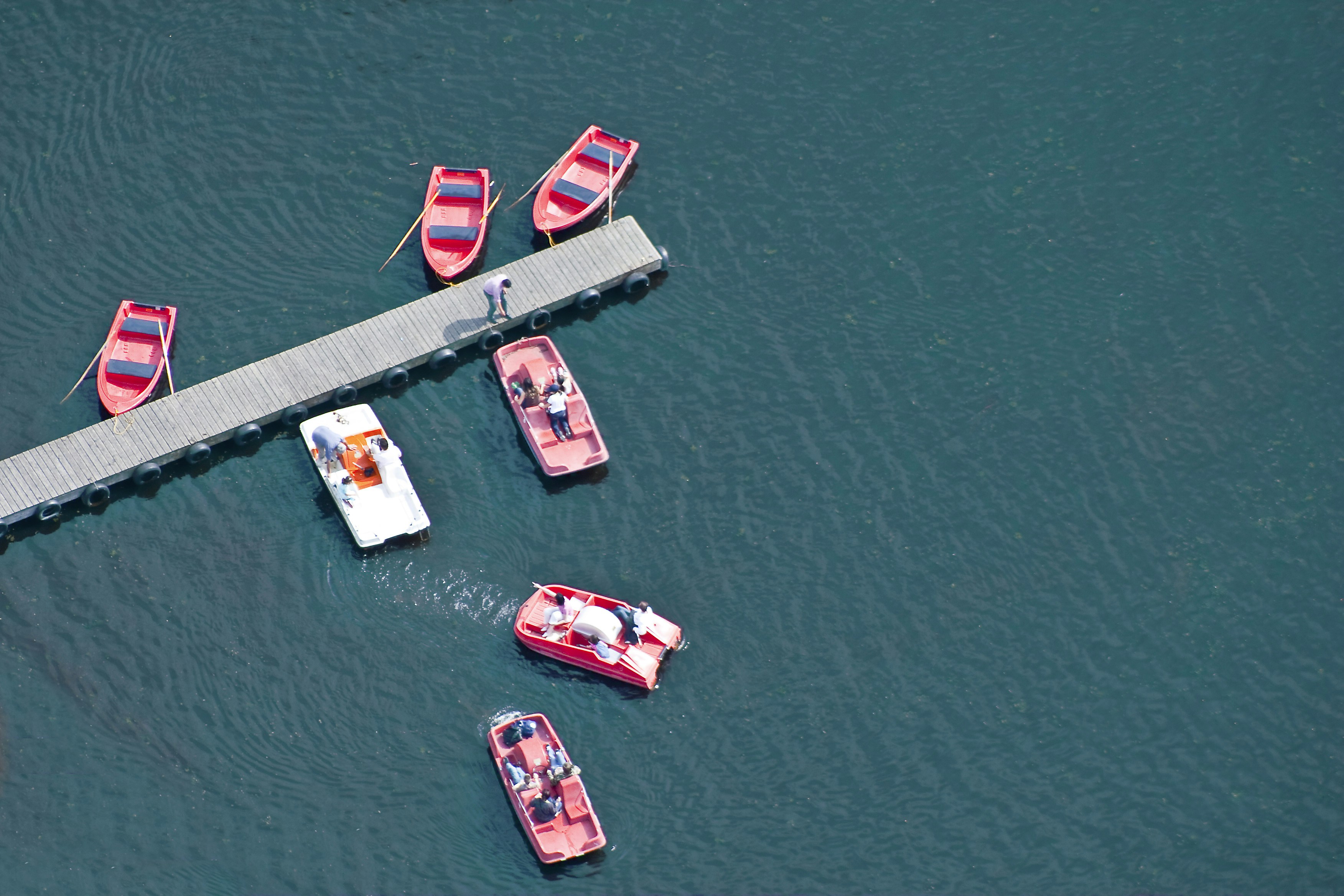 Pedal boats and rowboats moored alongside a wooden pier on a calm lake.