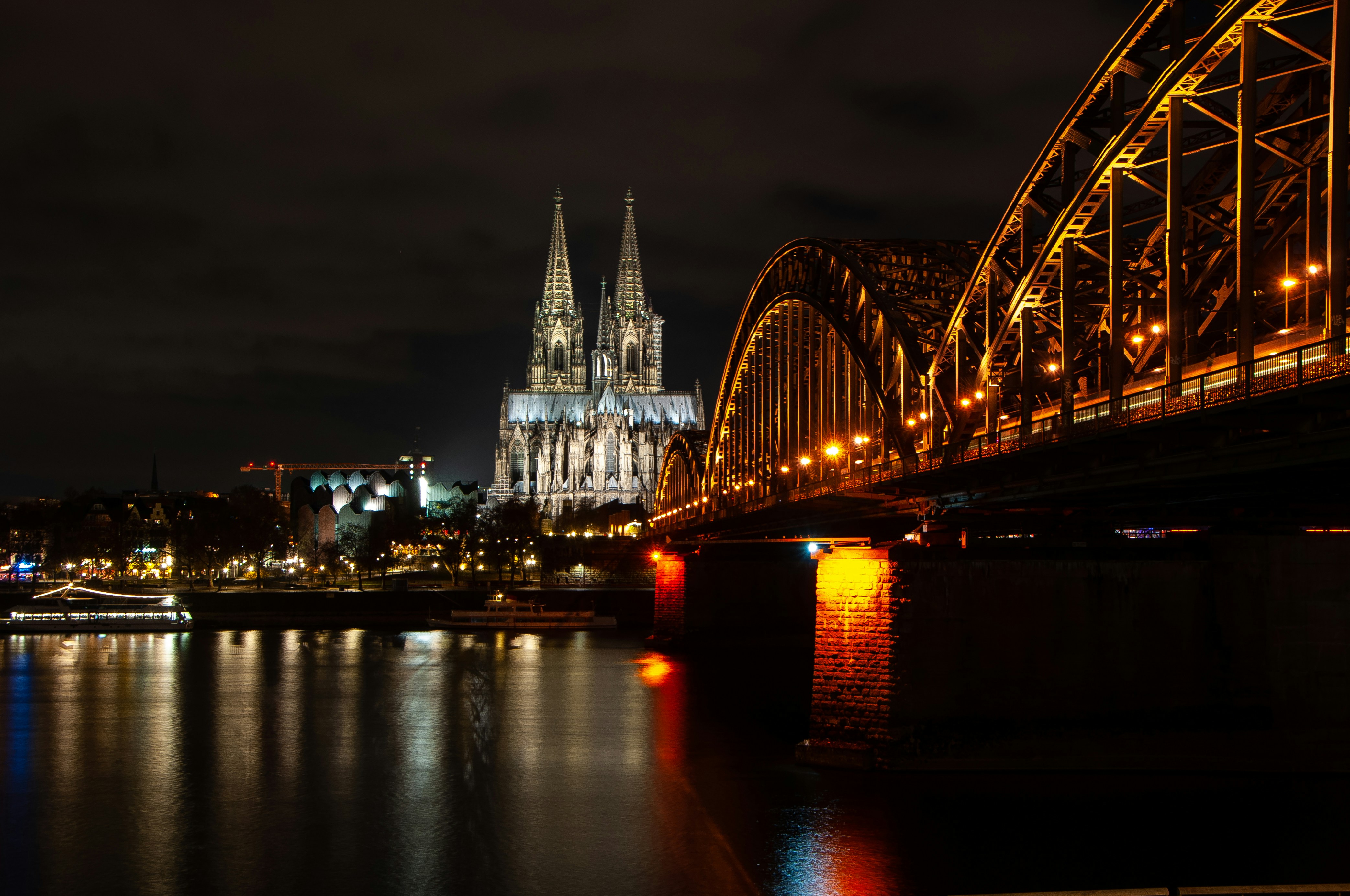 Gothic cathedral towers rise majestically against a night sky, illuminated by city lights, with a bridge arching gracefully in the foreground.