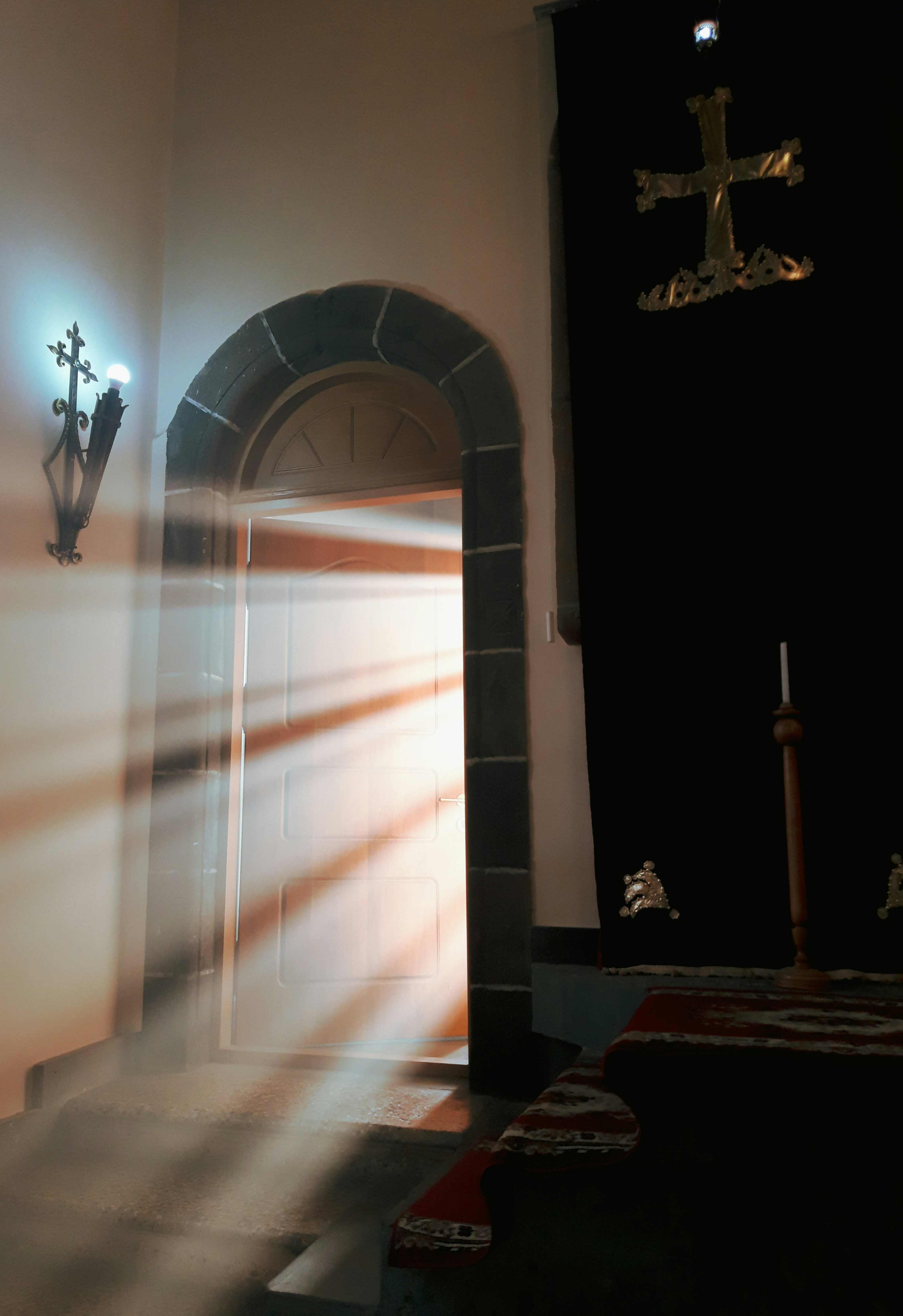 Sunbeams streaming through an arched doorway inside a dimly lit church, casting ethereal rays across the floor.