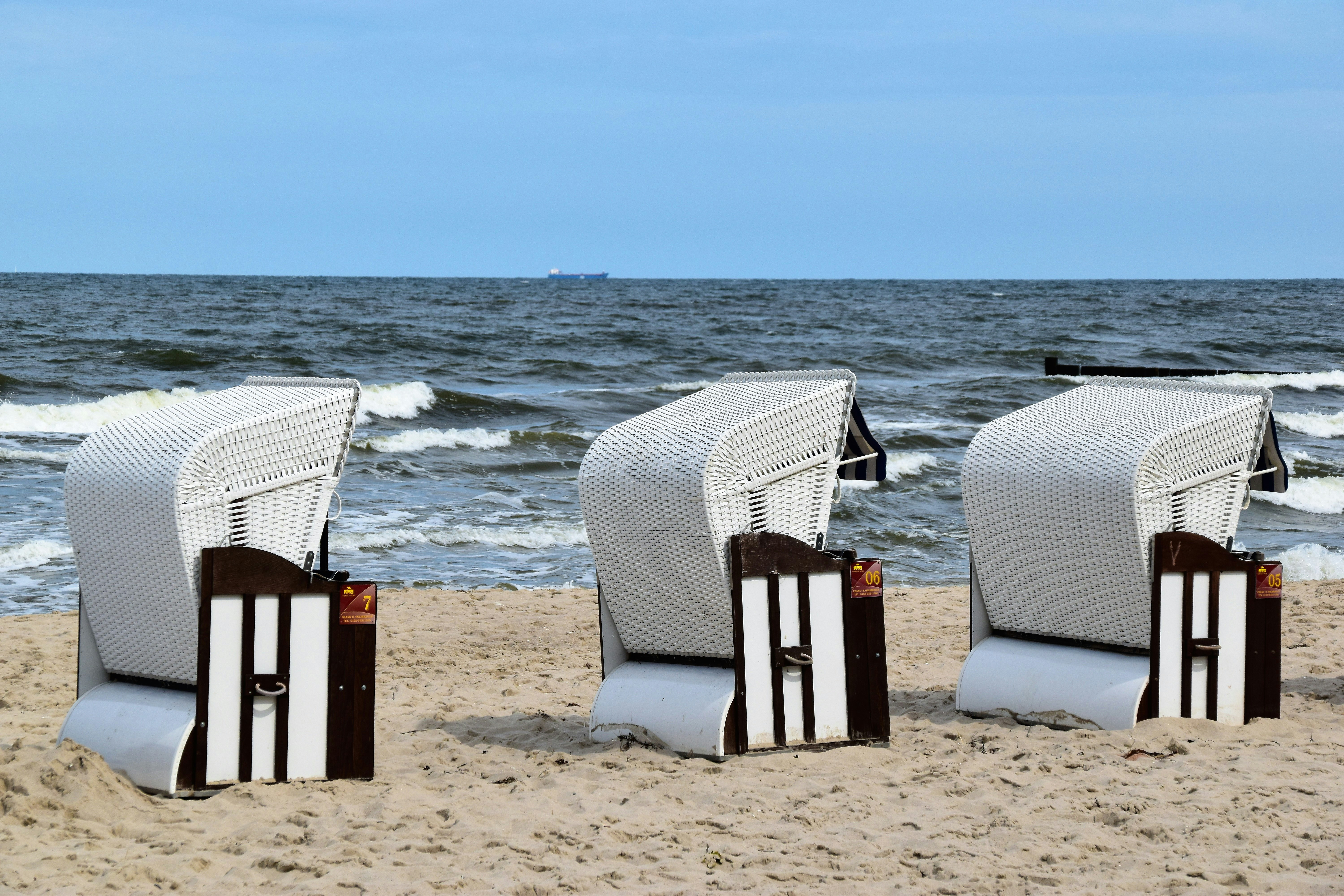 Three beach chairs arranged on sandy shore, facing gentle waves under a clear sky.