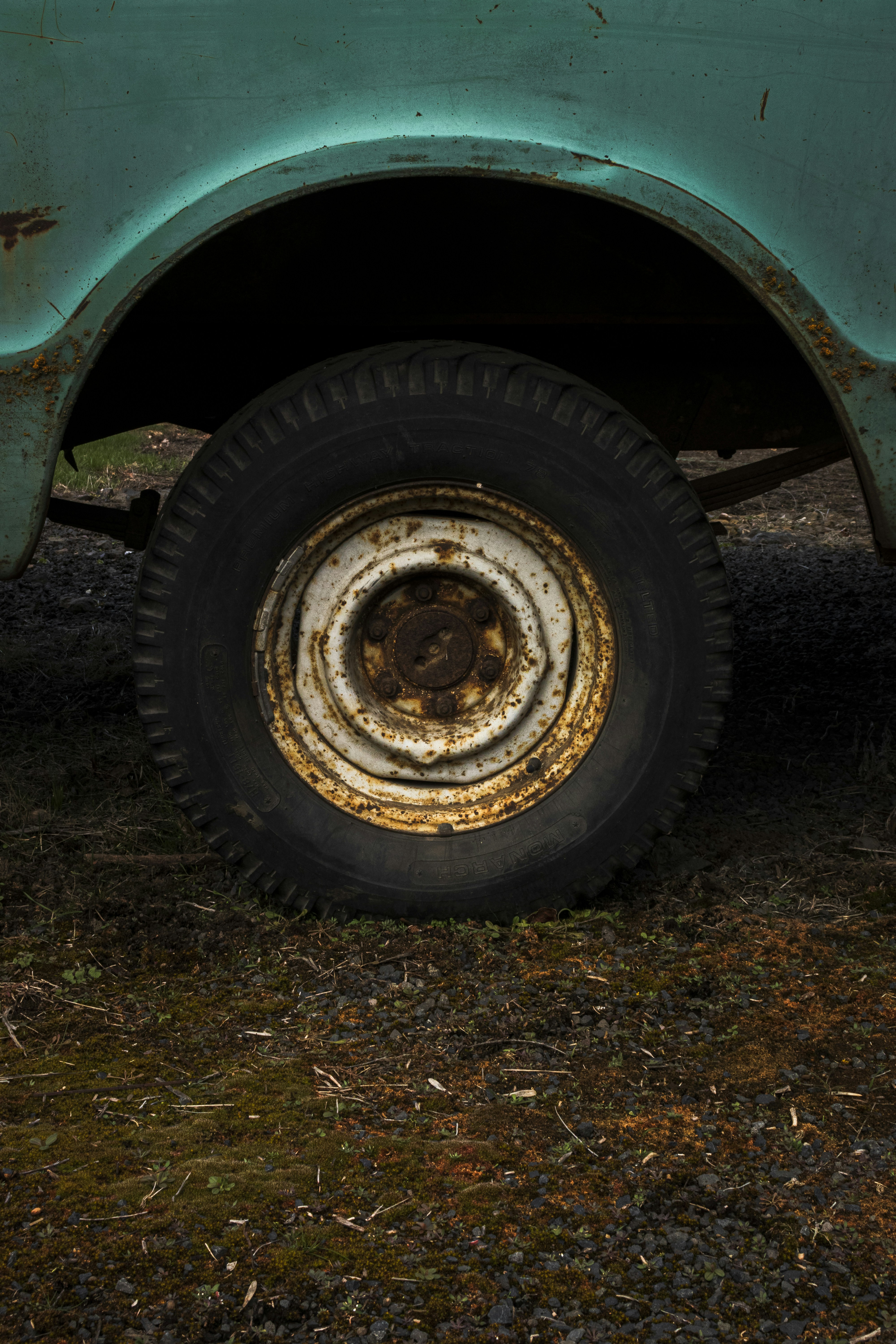 Close-up of a weathered truck wheel showcasing rust and decay against a textured ground. The scene evokes a sense of nostalgia and the passage of time.