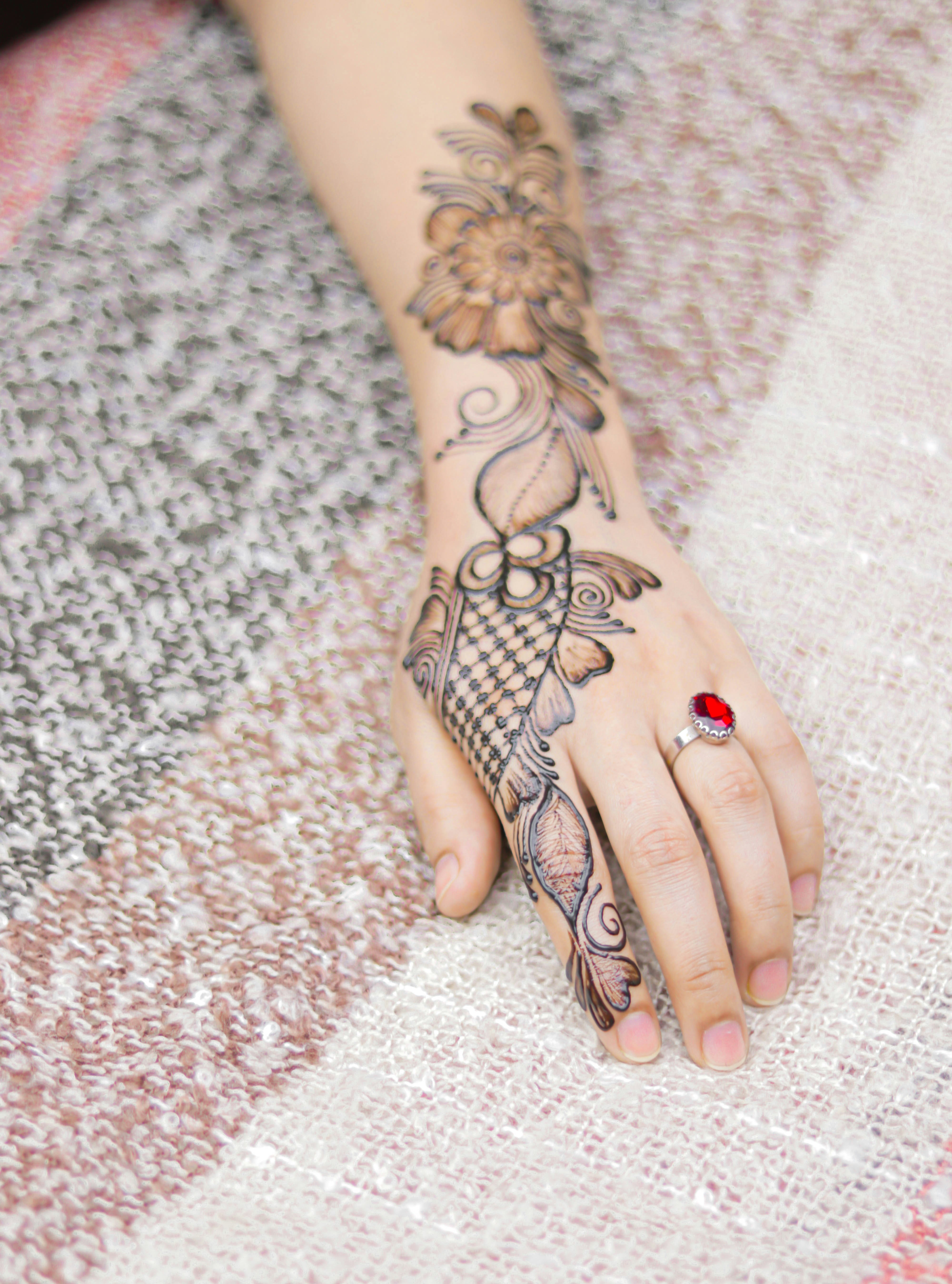 Detailed henna design with floral motifs on a hand, adorned with a red gemstone ring.