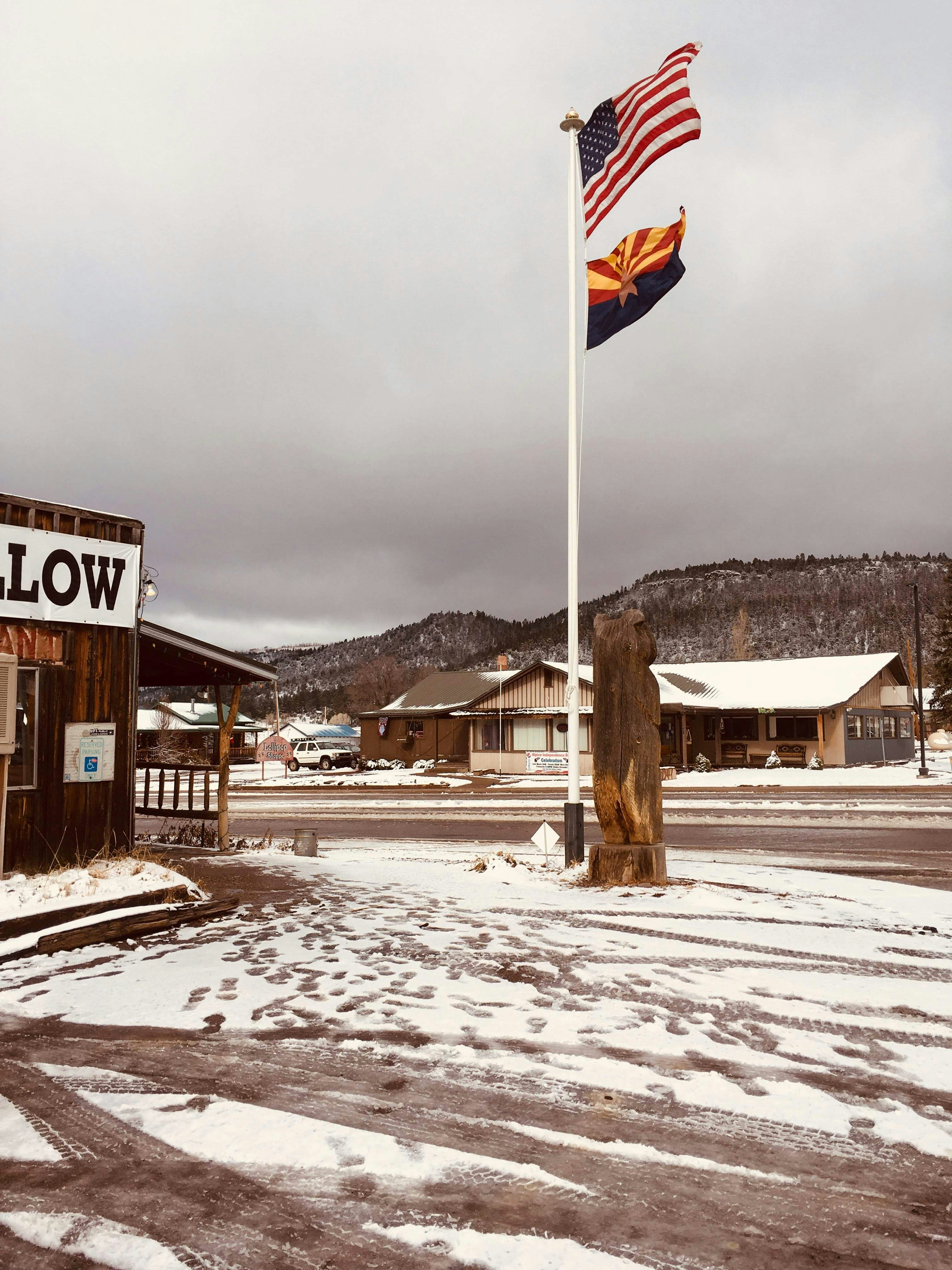 American and Arizona flags waving proudly against a snowy backdrop, with rustic buildings framing the scene.