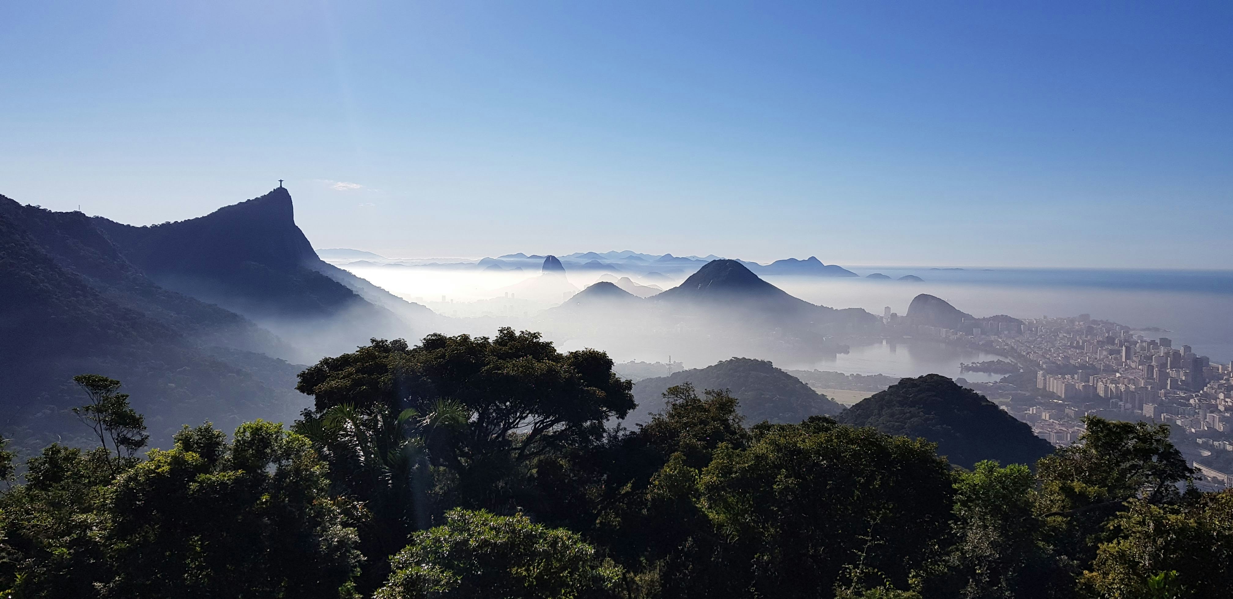 Lush green hills under a misty layer with cityscape and mountains in the distance.