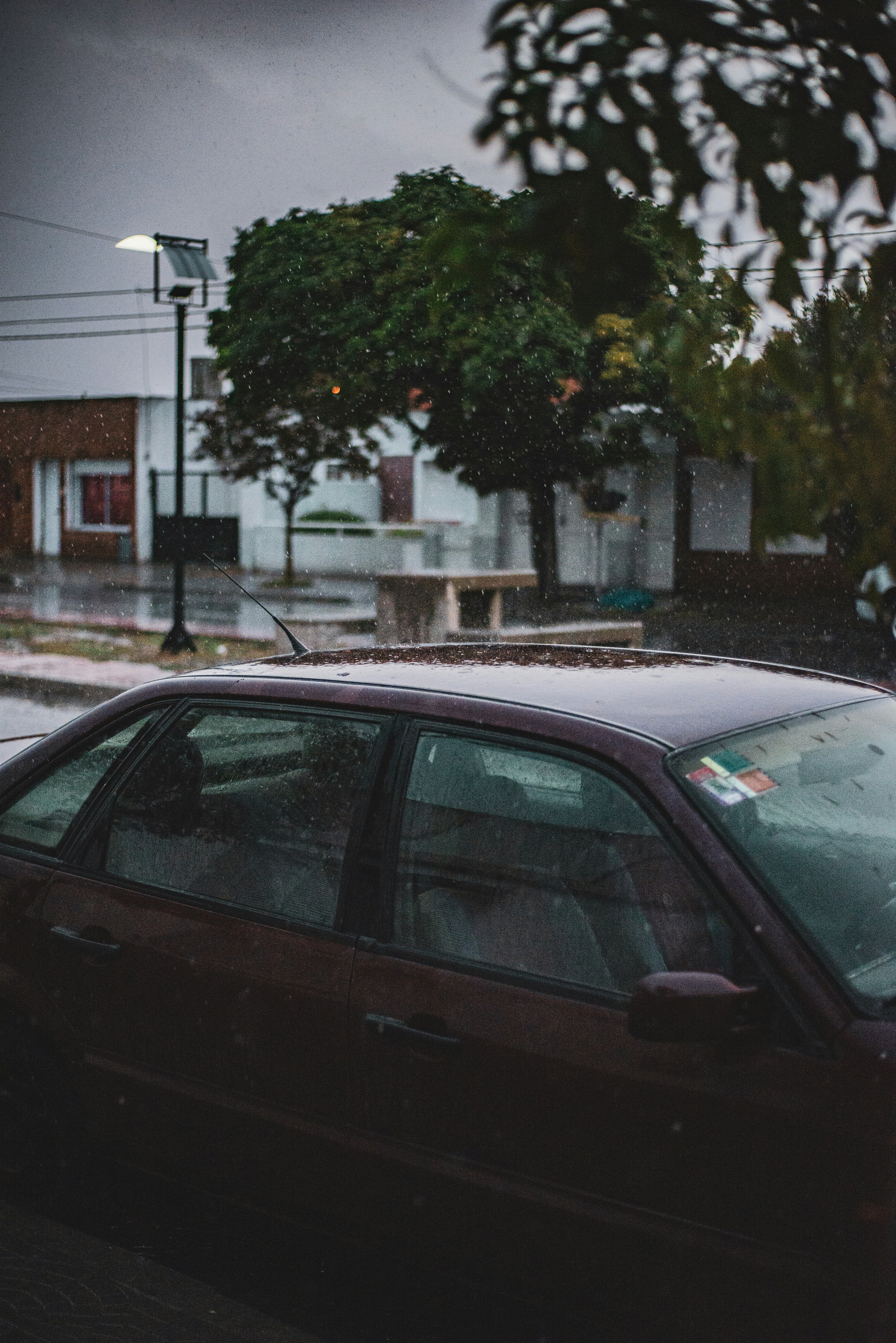 Rain-Slicked Sedan: a maroon pause under grey skies