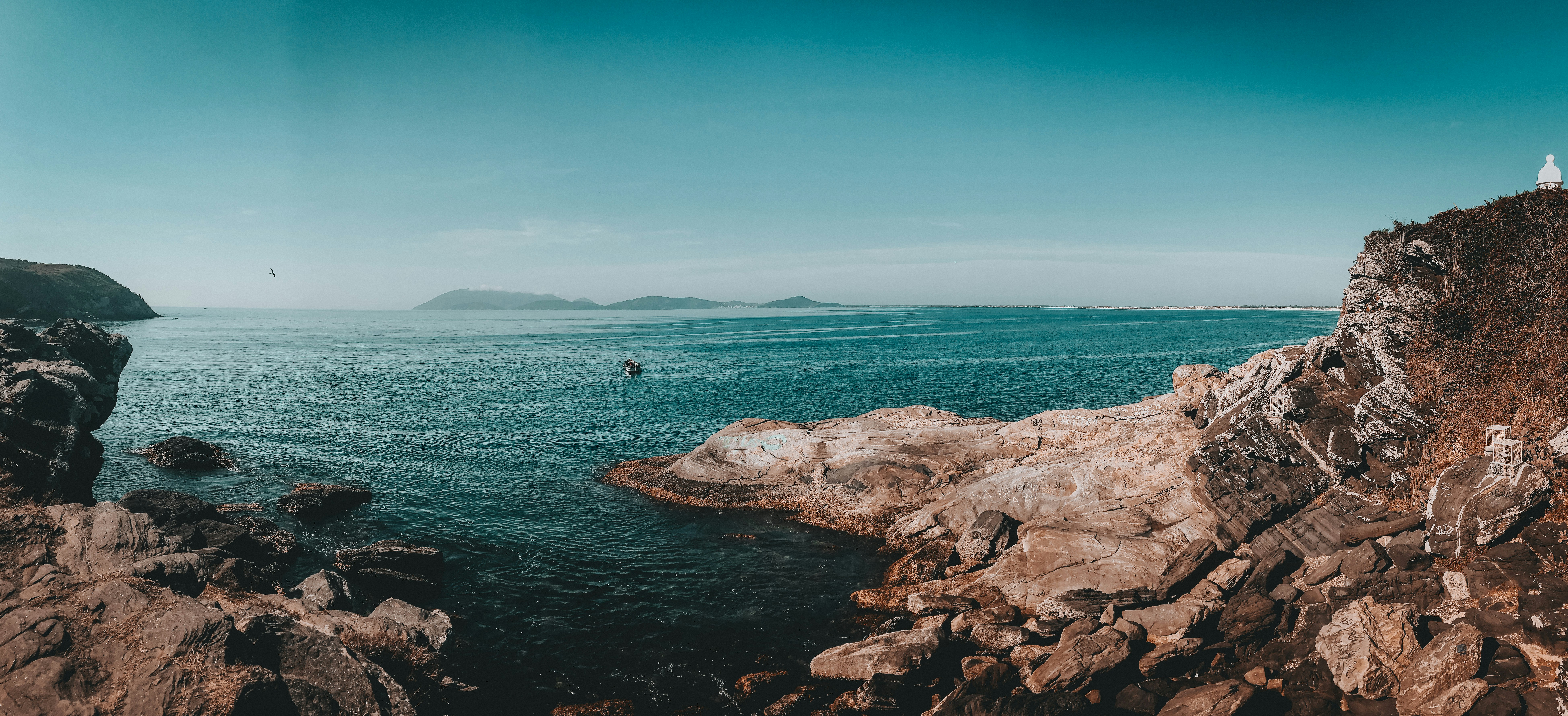 Panoramic view of a rocky coastline meeting a tranquil sea under a clear blue sky.