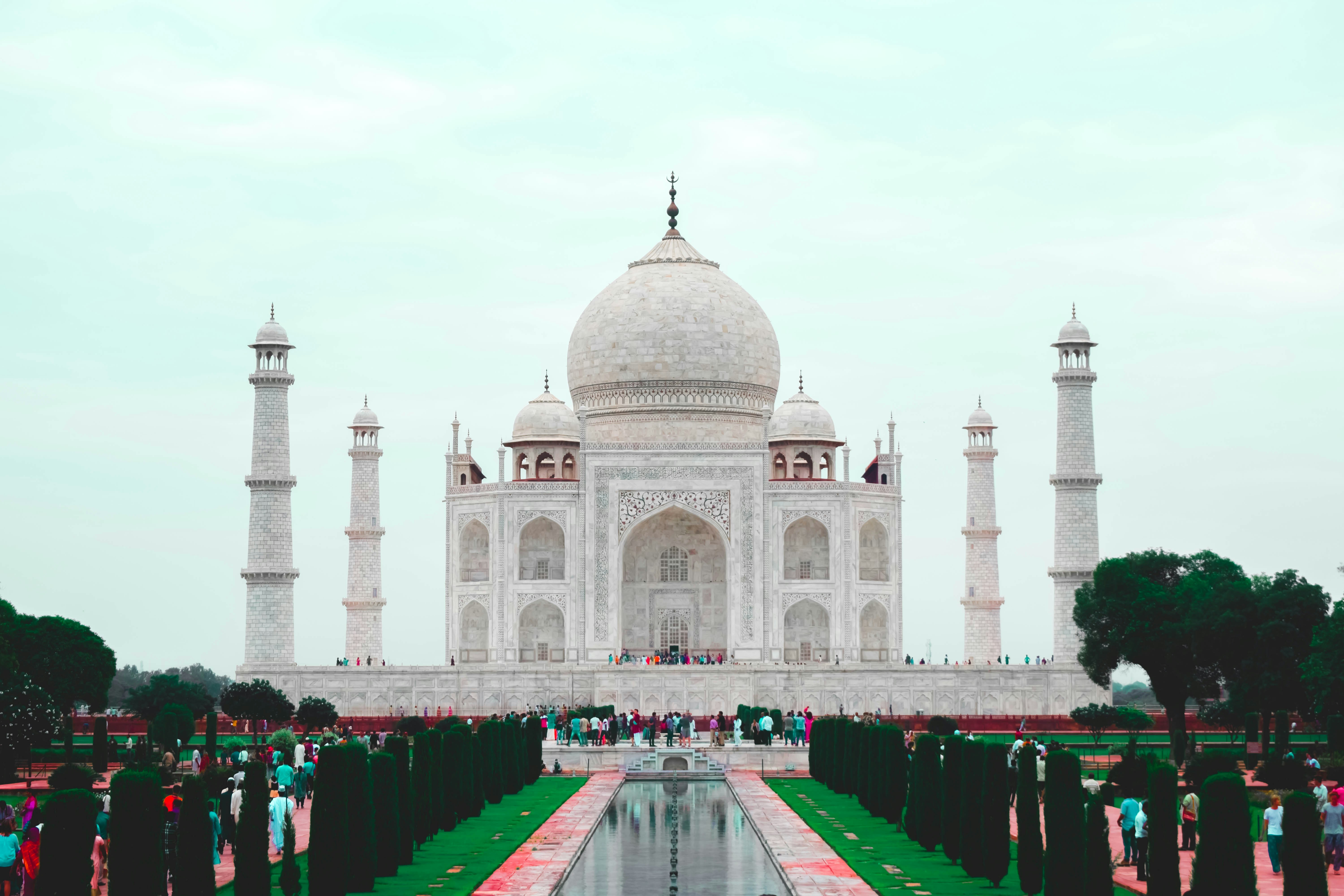 Taj Mahal standing majestically amidst lush gardens and reflective pools, with visitors exploring its grandeur.