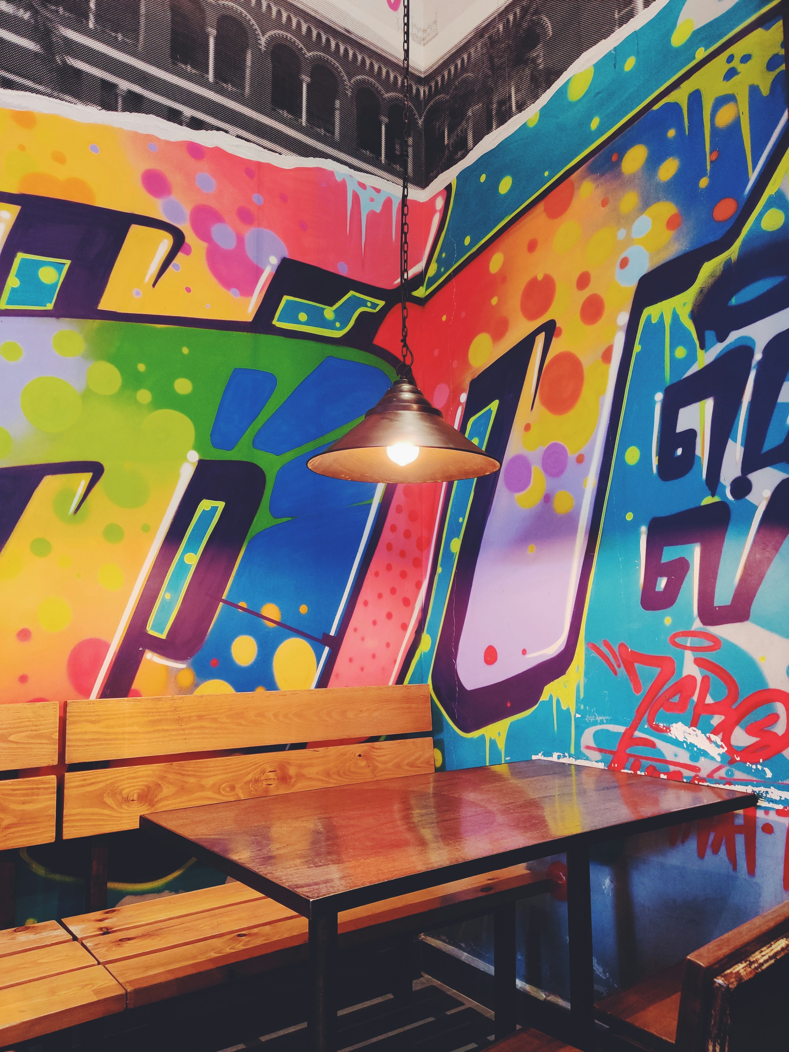 Colorful graffiti adorns the walls of a cozy café, complemented by a stylish pendant light and wooden seating. The lively atmosphere invites creativity and relaxation.