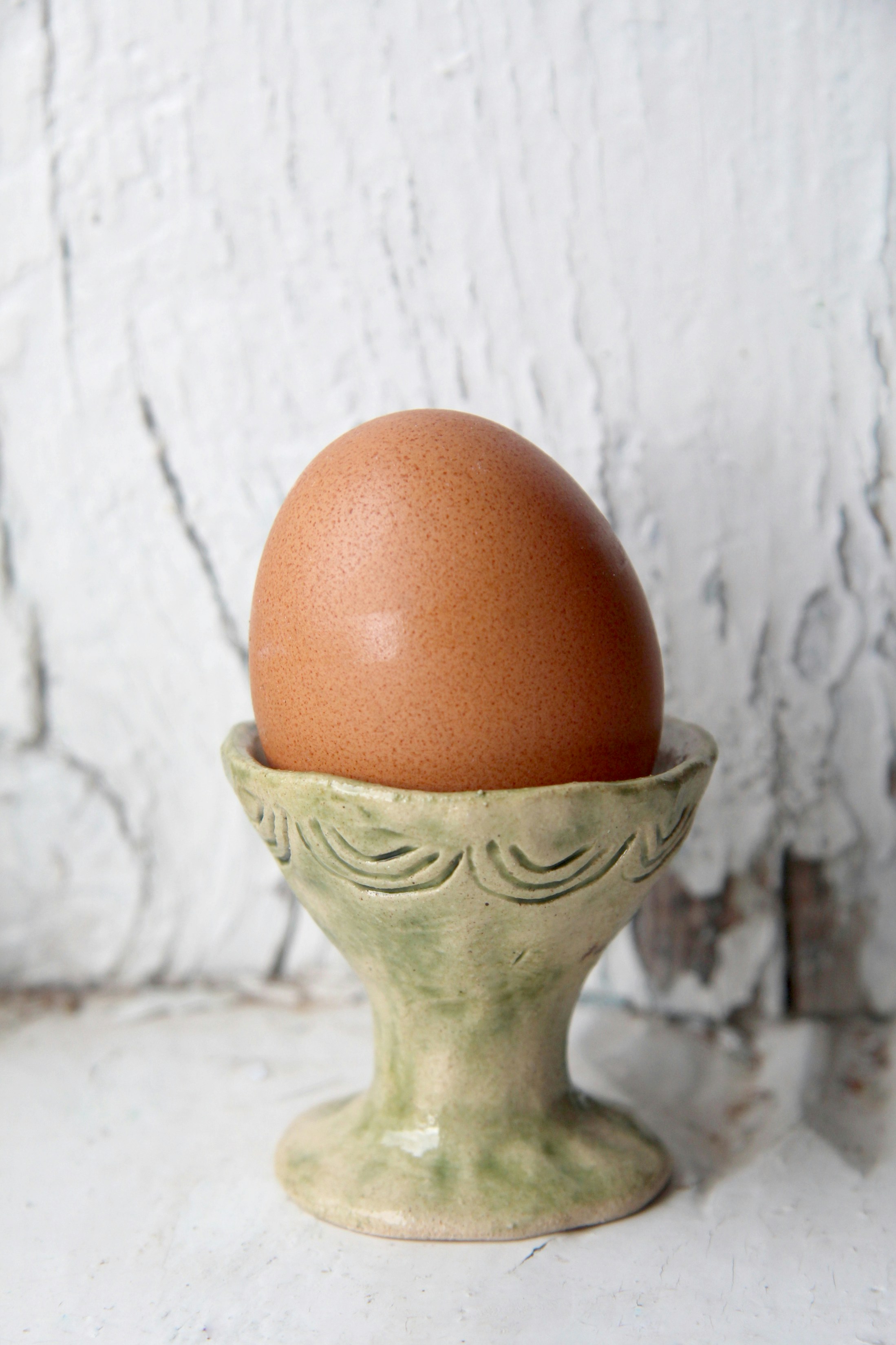 Quiet Sage: Egg Resting in a Pale Ceramic Cup Against Weathered White Wood