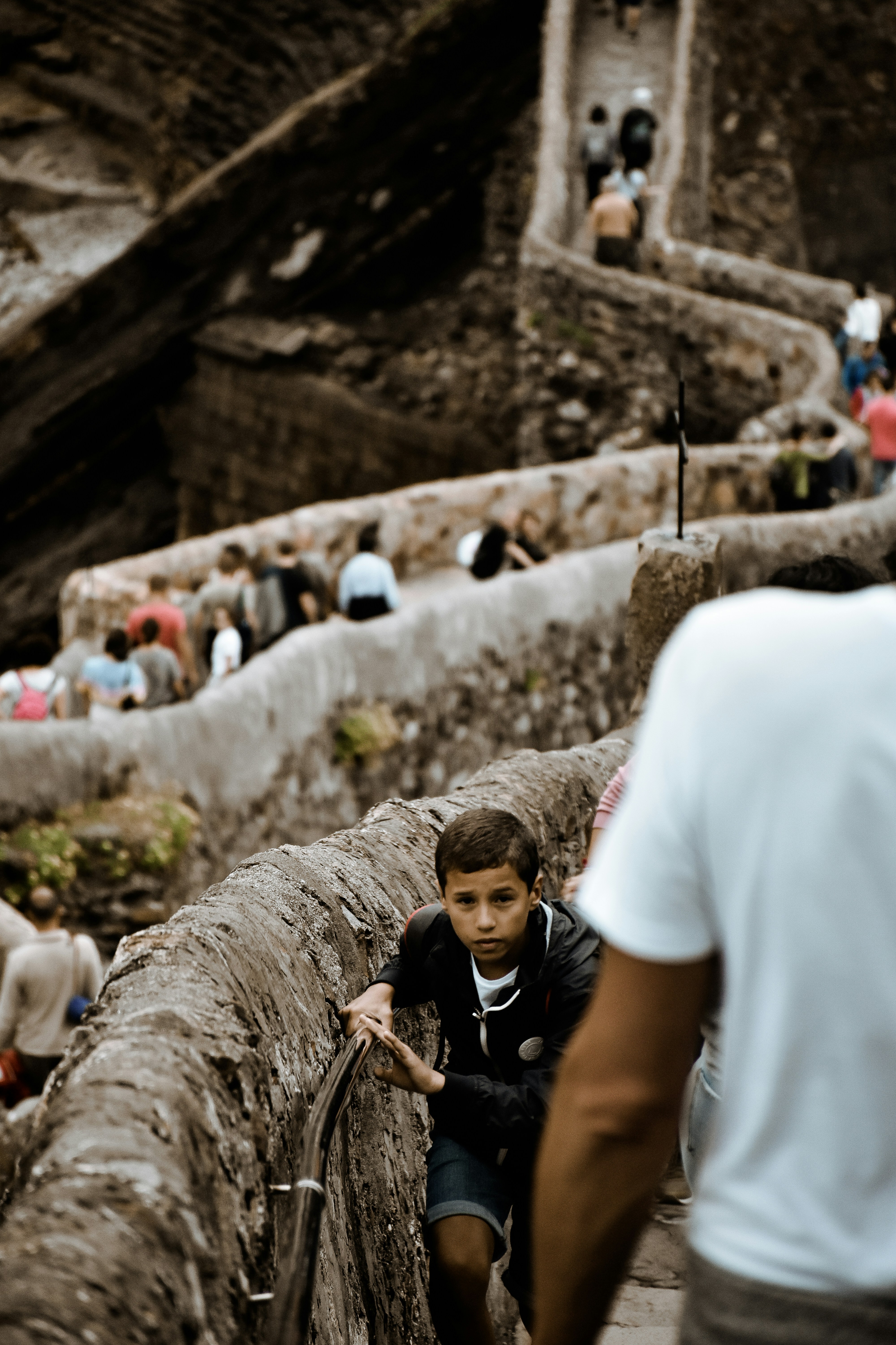 boy in black t-shirt and white pants sitting on rock during daytime