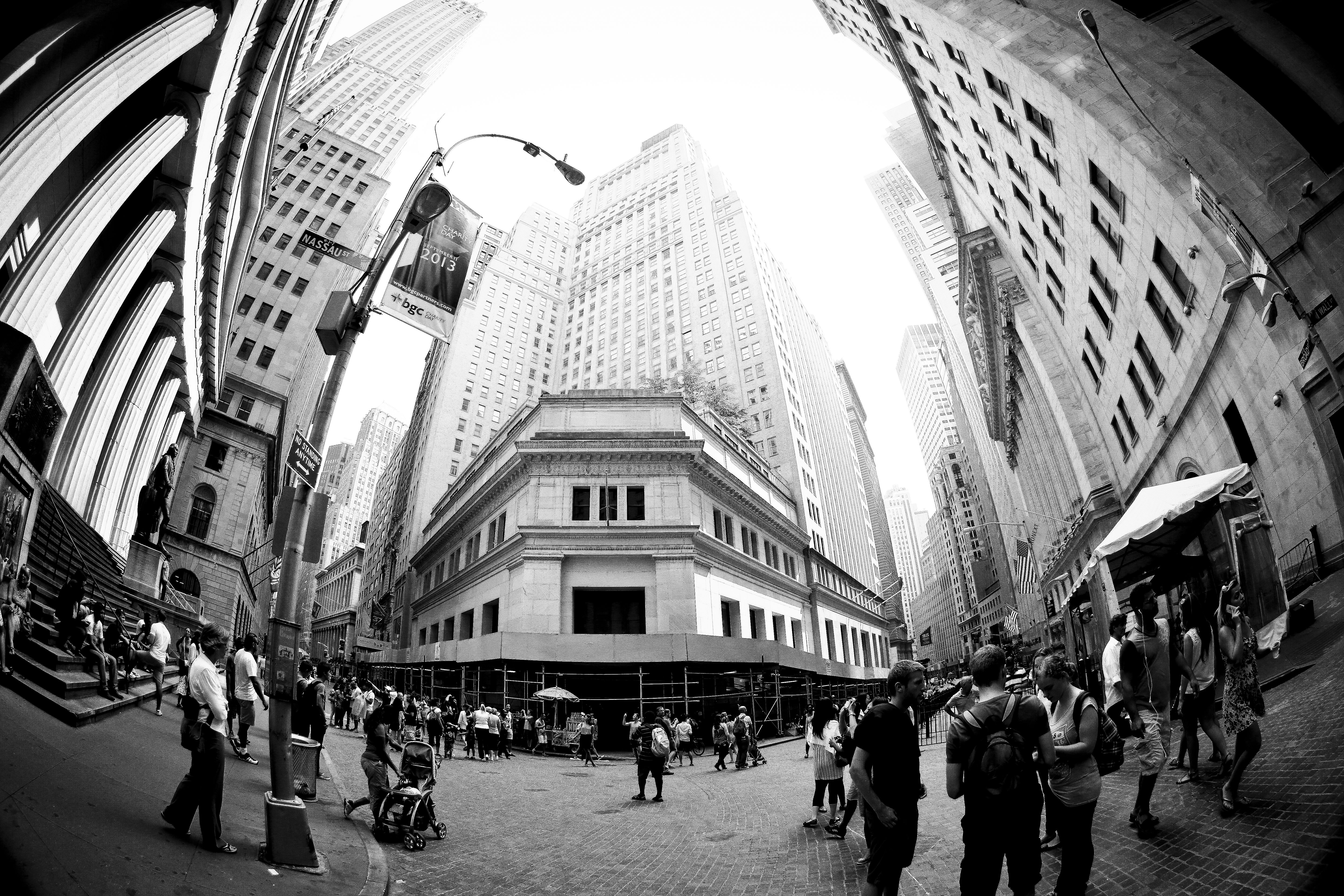 Historic building surrounded by bustling crowds in a vibrant urban setting, captured in black and white. The fisheye perspective emphasizes the towering structures above.