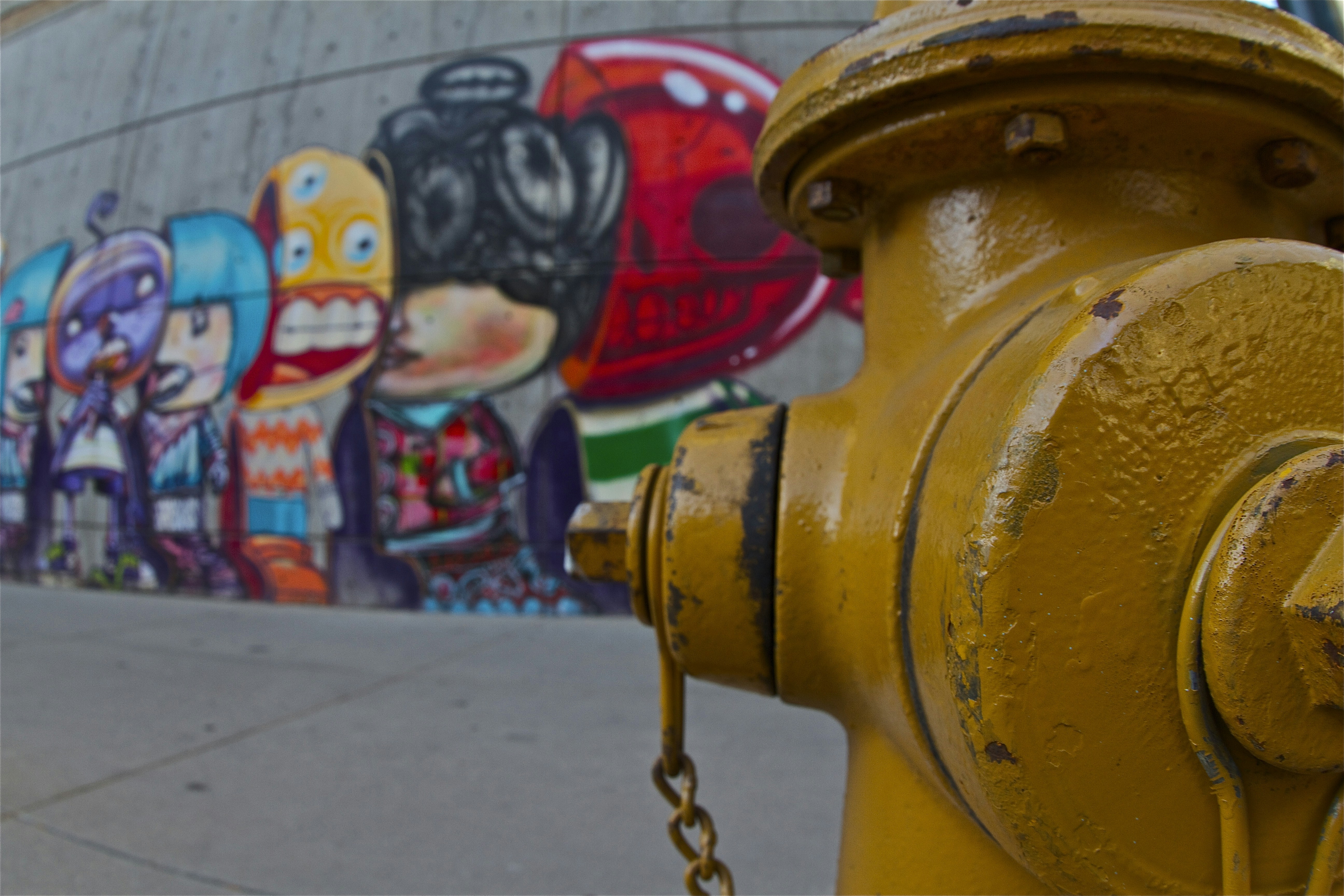 Vibrant street art featuring cartoonish characters painted on a concrete wall, juxtaposed with a bright yellow fire hydrant in the foreground.