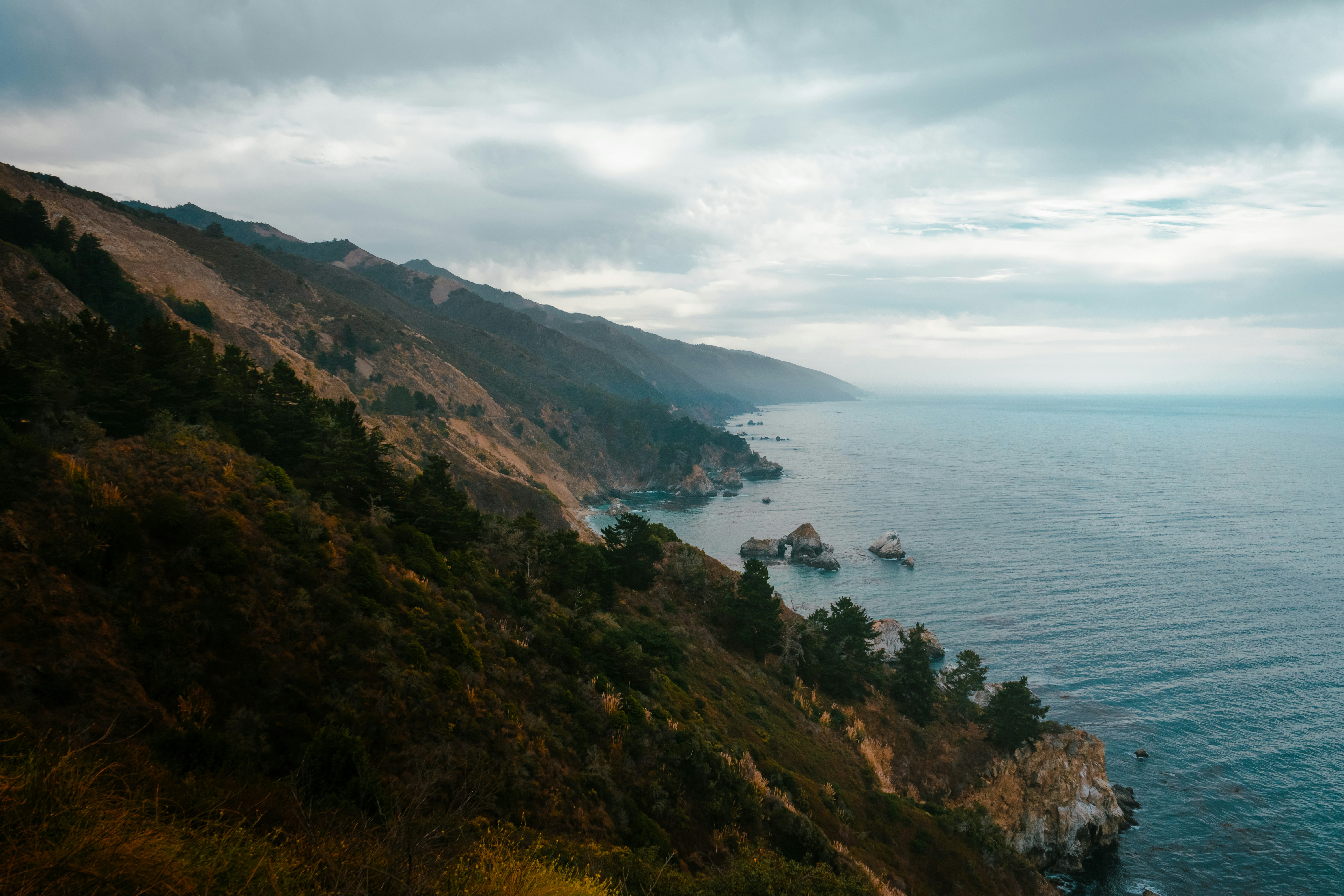Dramatic coastal landscape featuring rugged cliffs and tranquil waters under a cloudy sky.