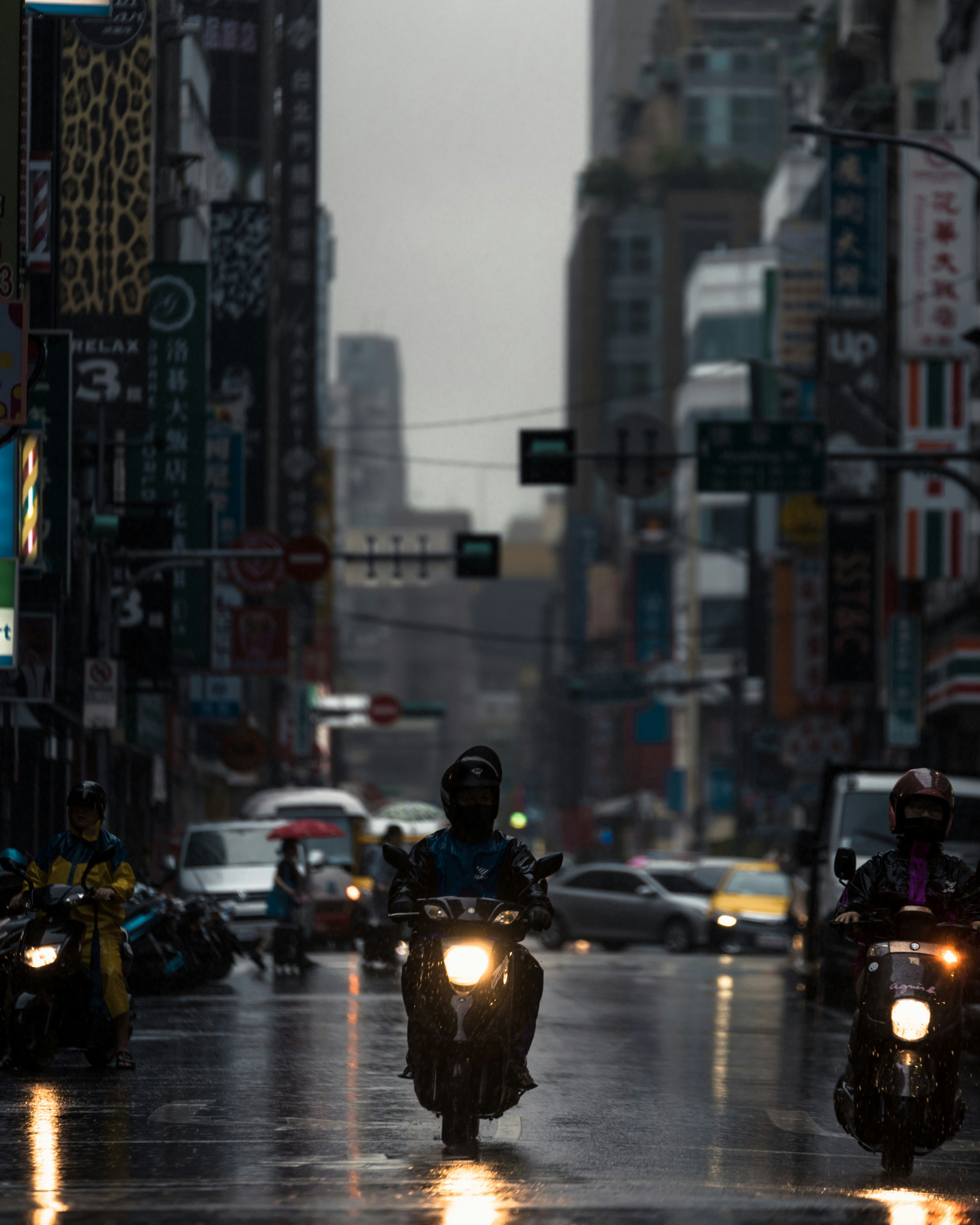 Motorcyclists navigating a rain-soaked urban street, illuminated by headlights and surrounded by vibrant neon signs.