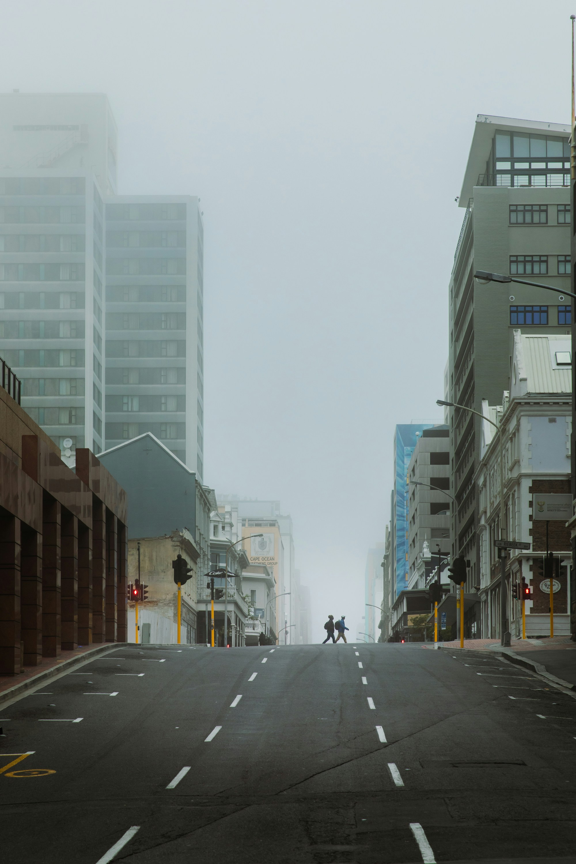 Two figures walking hand in hand down a foggy city street, flanked by modern buildings fading into the mist.