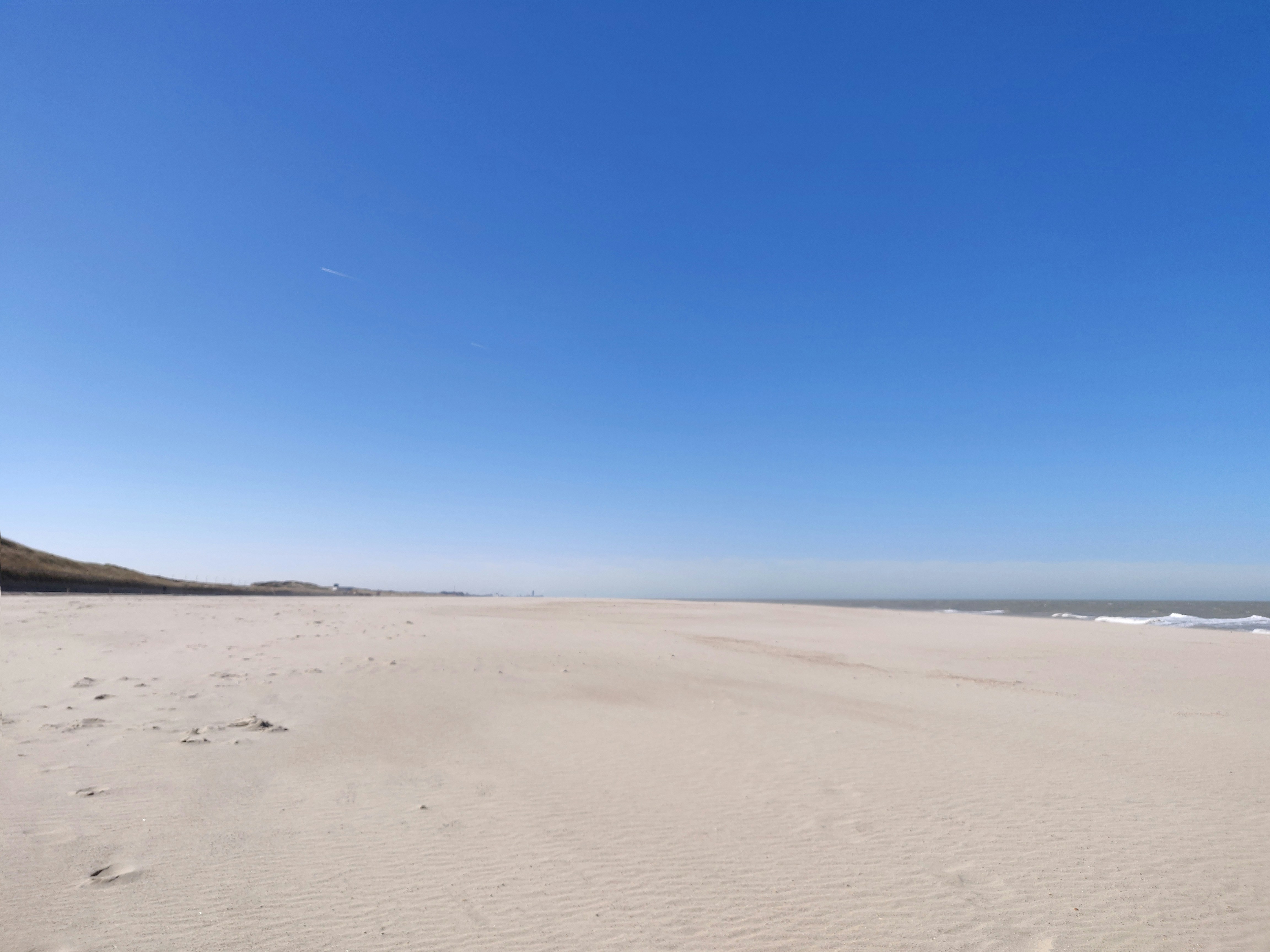 Vast sandy beach stretching under a bright blue sky with distant waves on the horizon.