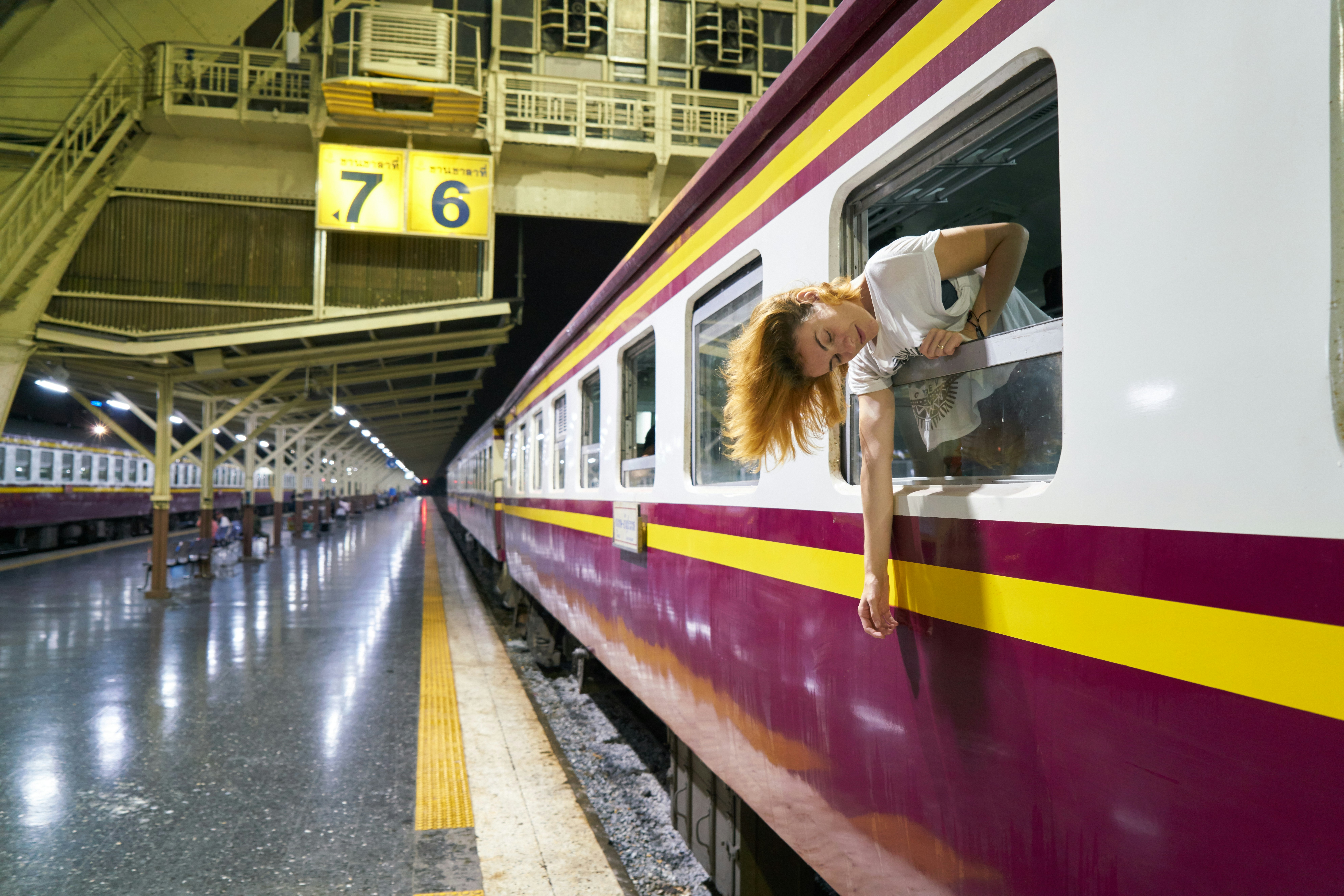 Person leaning out of a train window at a dimly lit platform under a large sign displaying numbers.