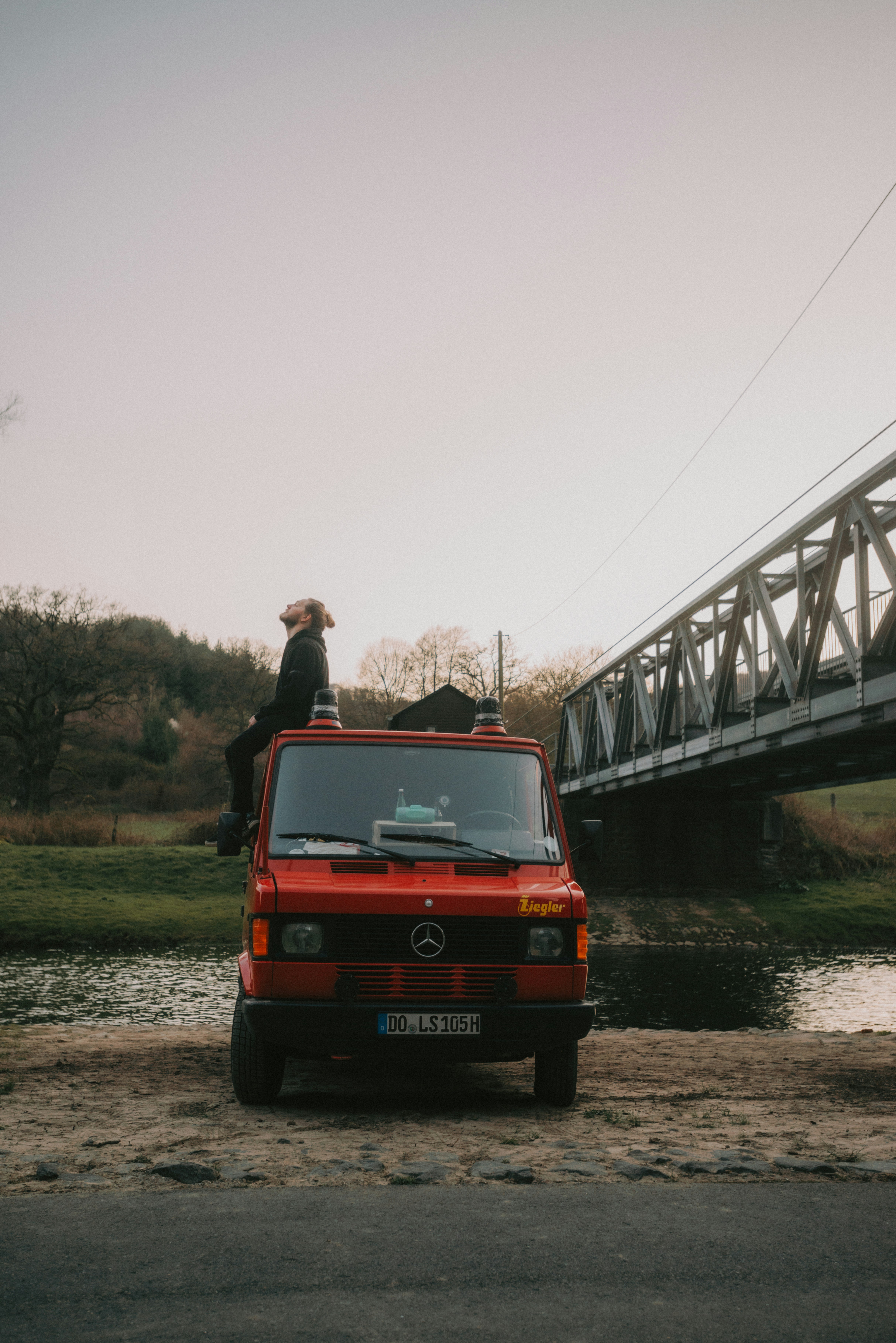 man in black jacket standing beside red car under bridge during daytime
