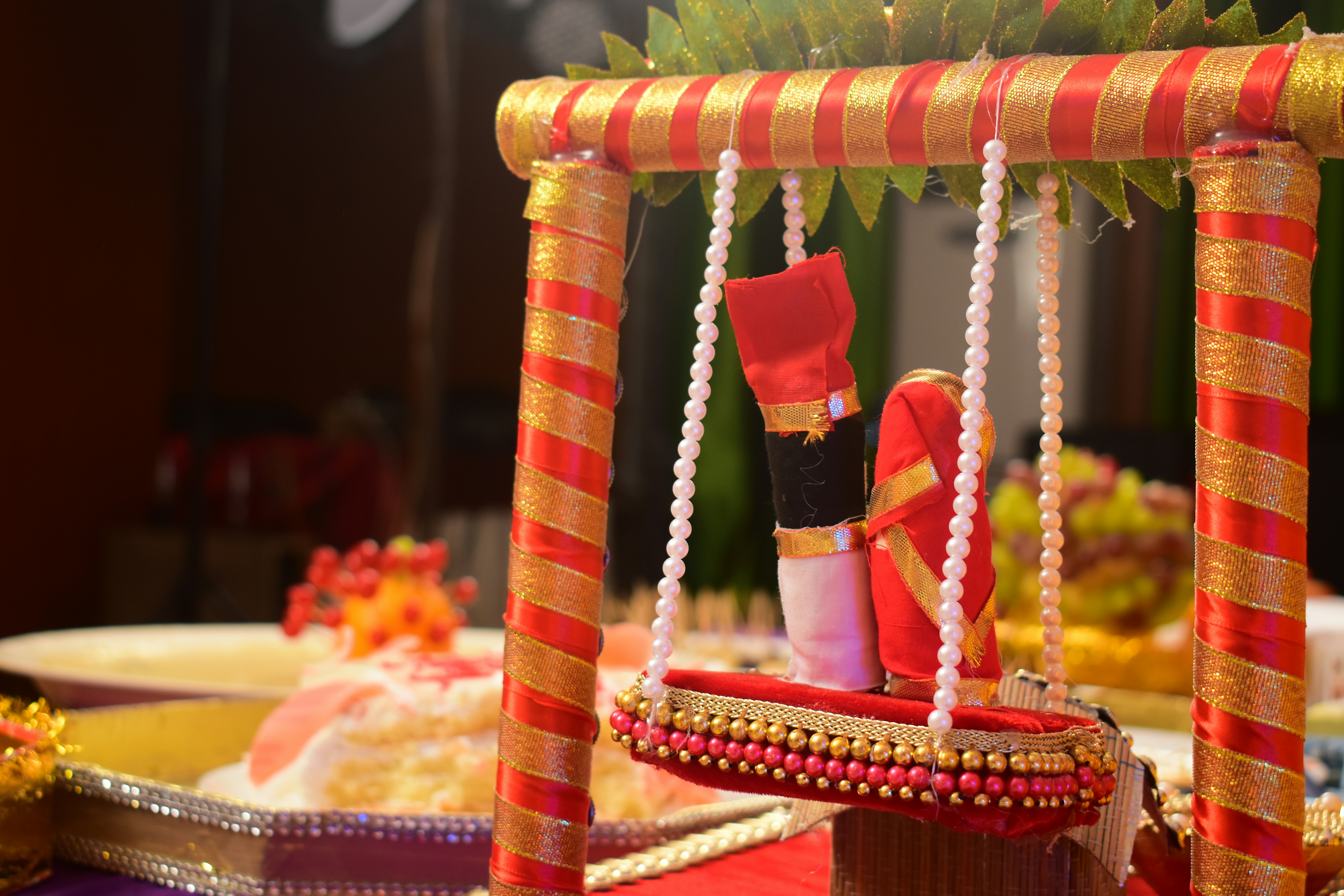 Colorful miniature swing adorned with decorative beads and fabric, set against a festive backdrop with treats and decorations.