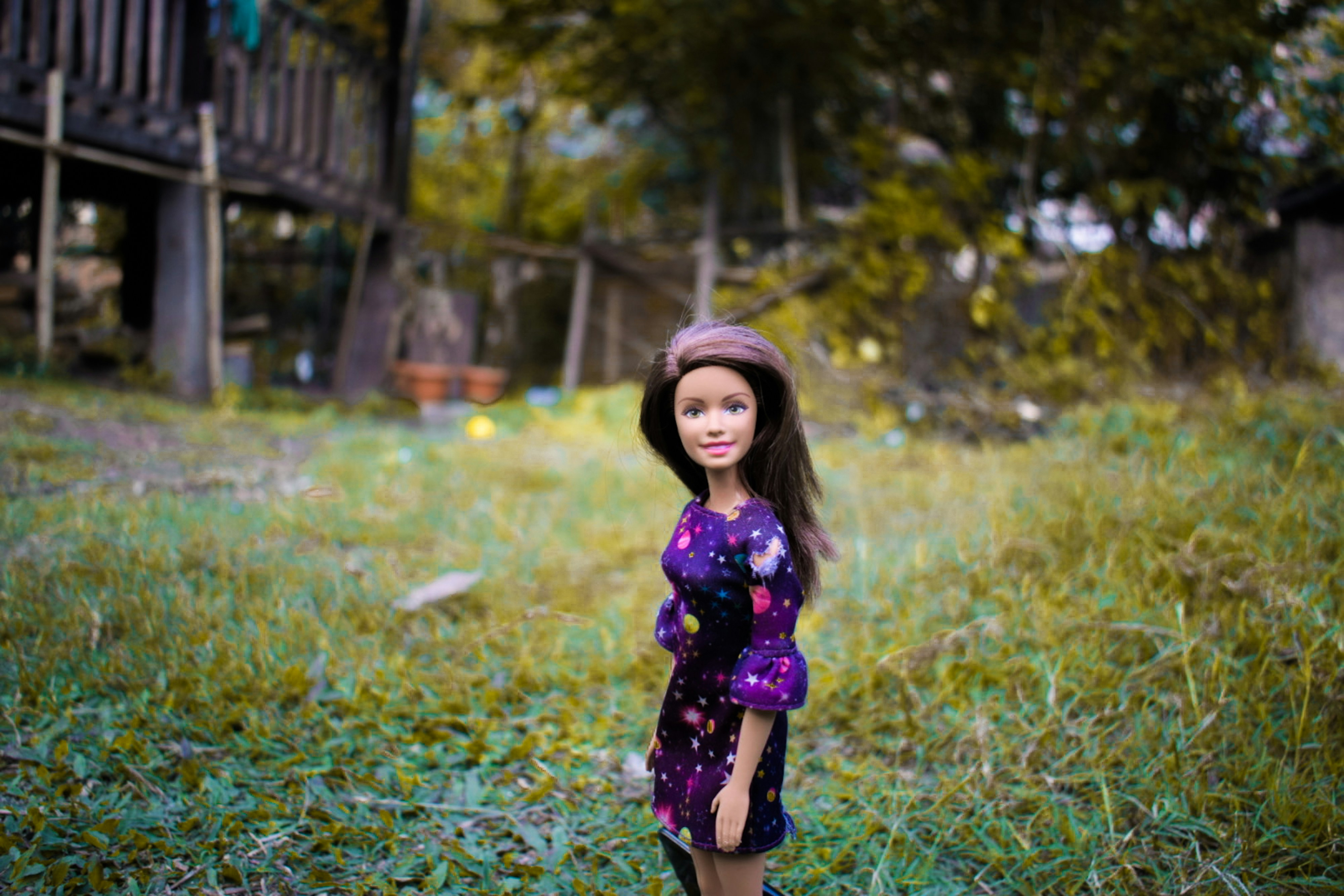A doll in a colorful dress stands amidst vibrant greenery, exuding a playful charm. The natural backdrop enhances the scene's whimsical feel.