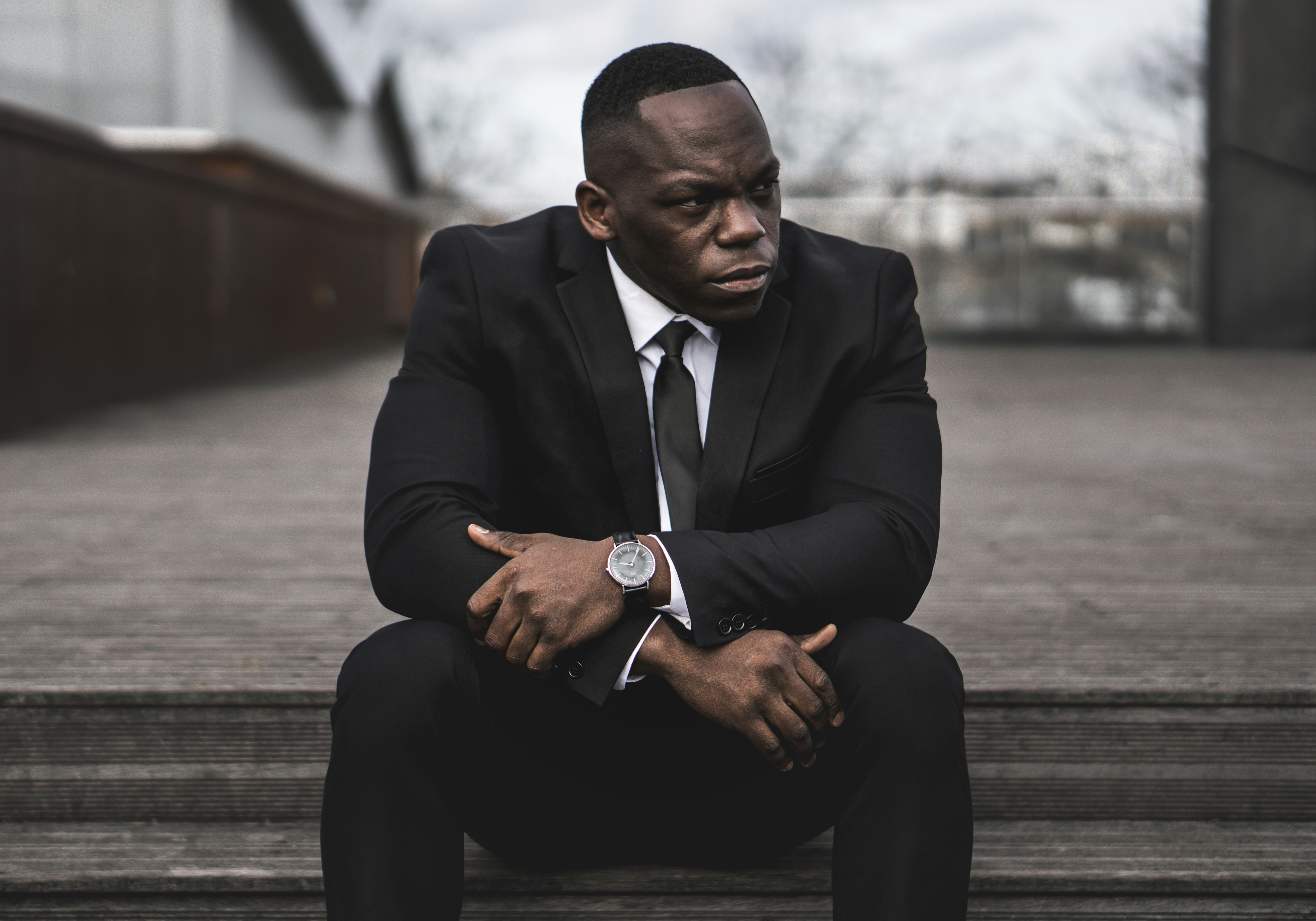 A well-dressed man seated on stairs, deep in thought, exuding confidence and sophistication.