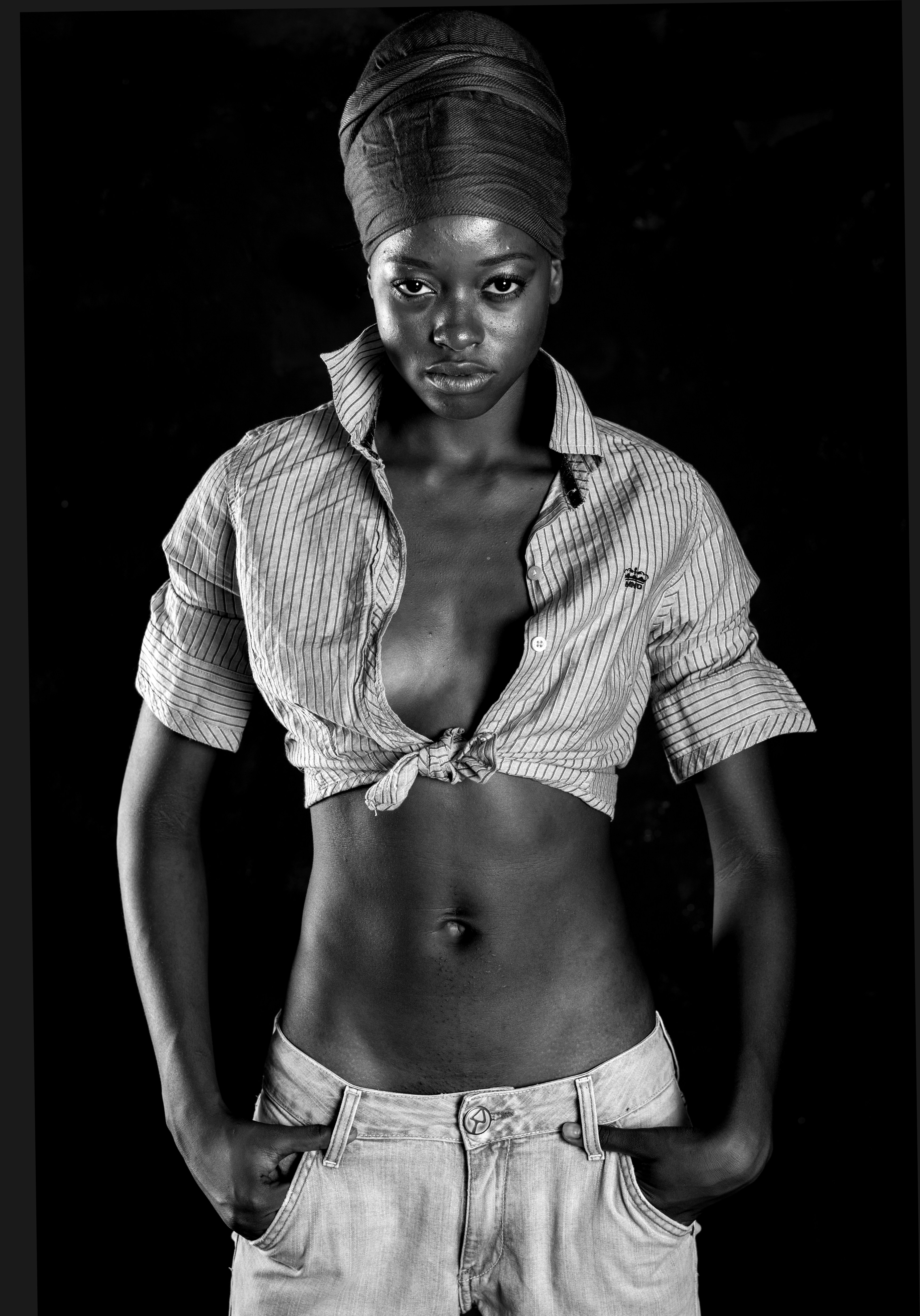 A confident model in a cropped striped shirt and denim, striking a pose with hands in pockets against a dark backdrop.