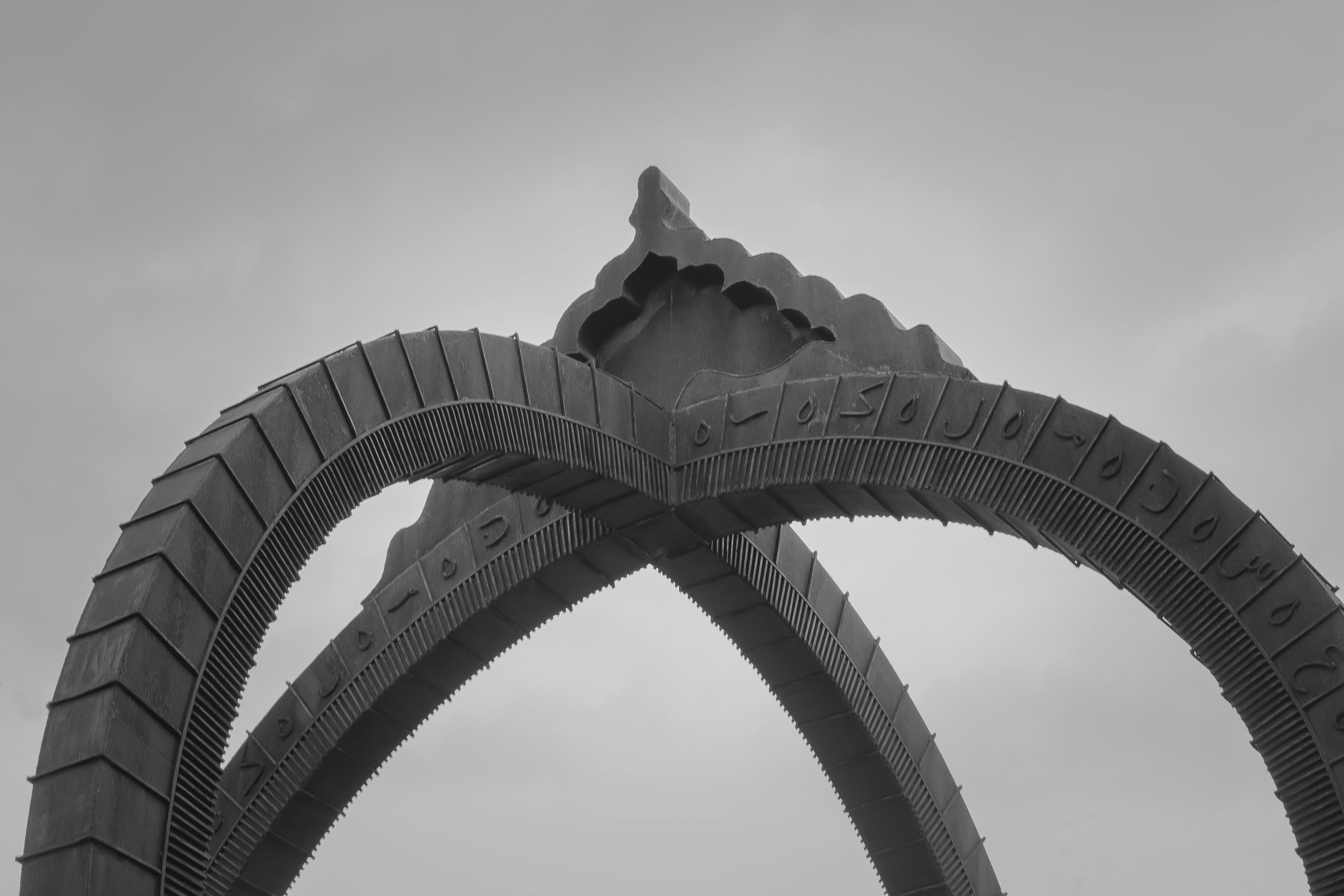 Abstract sculpture featuring interlocking arches, showcasing intricate details and a dramatic silhouette against a cloudy sky.