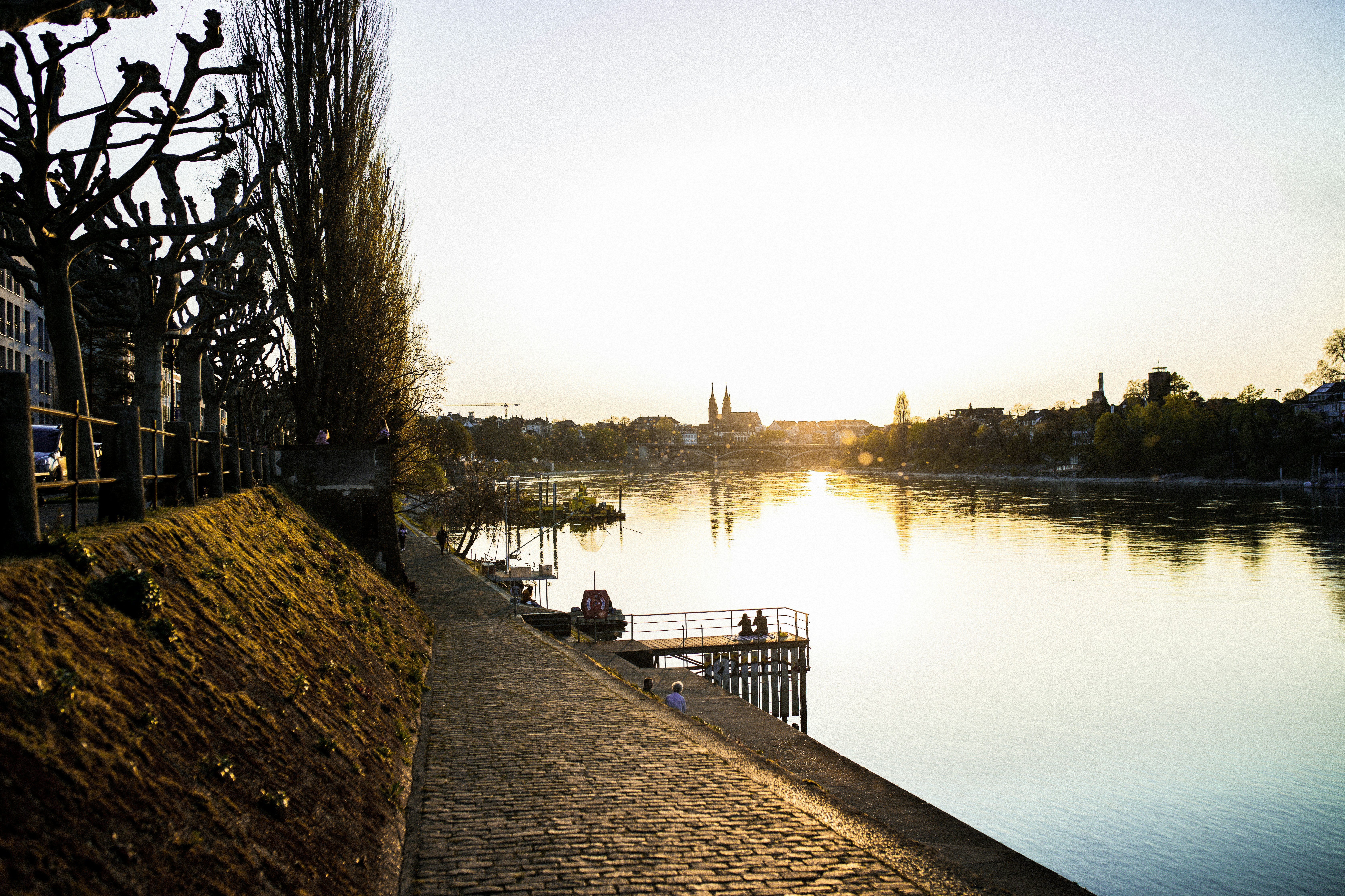Sunset over a calm river with silhouetted trees and a distant dock.