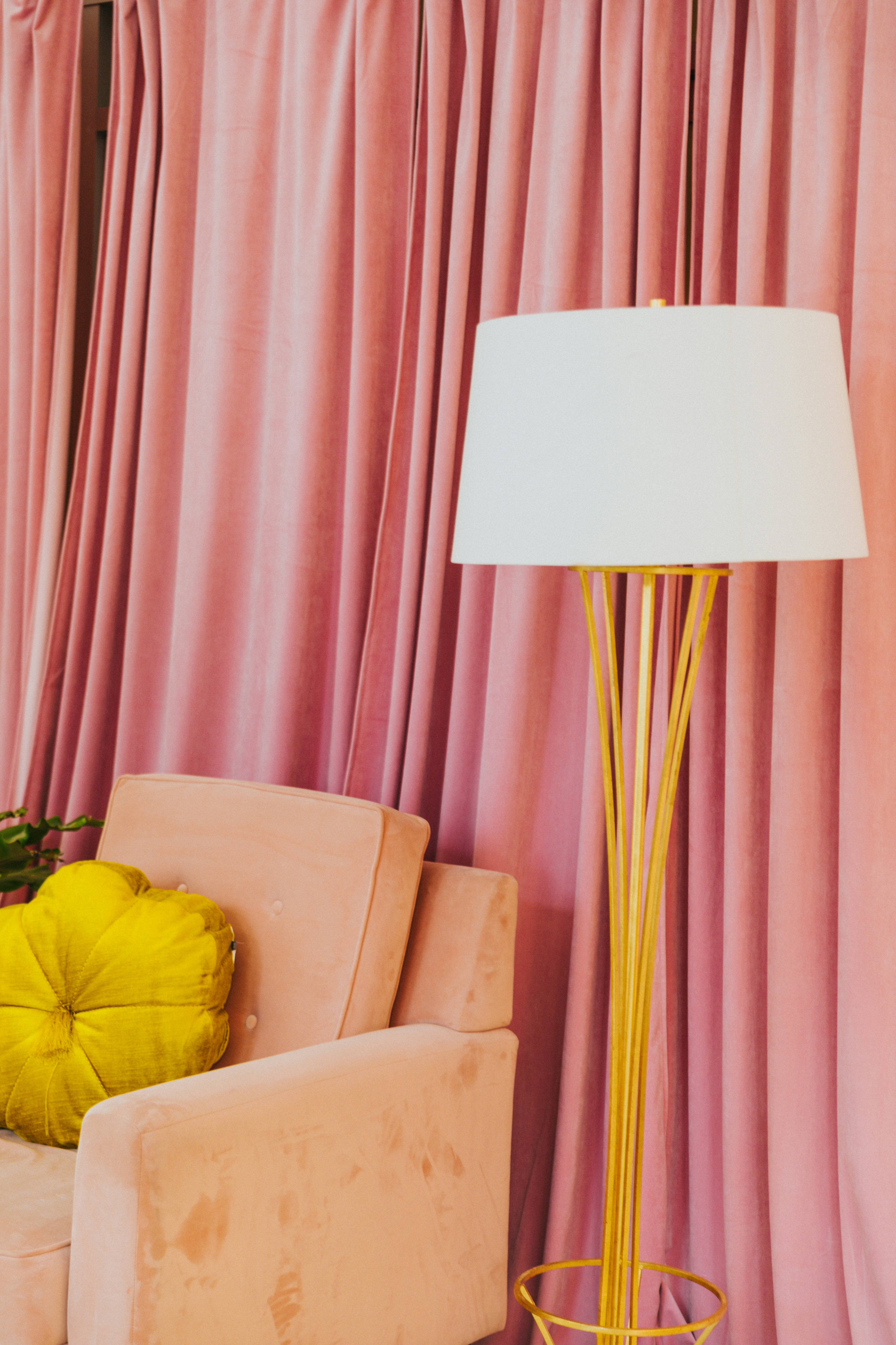 A soft pink armchair with a yellow cushion beside a stylish floor lamp, set against flowing pink curtains. The scene exudes a warm, inviting atmosphere.