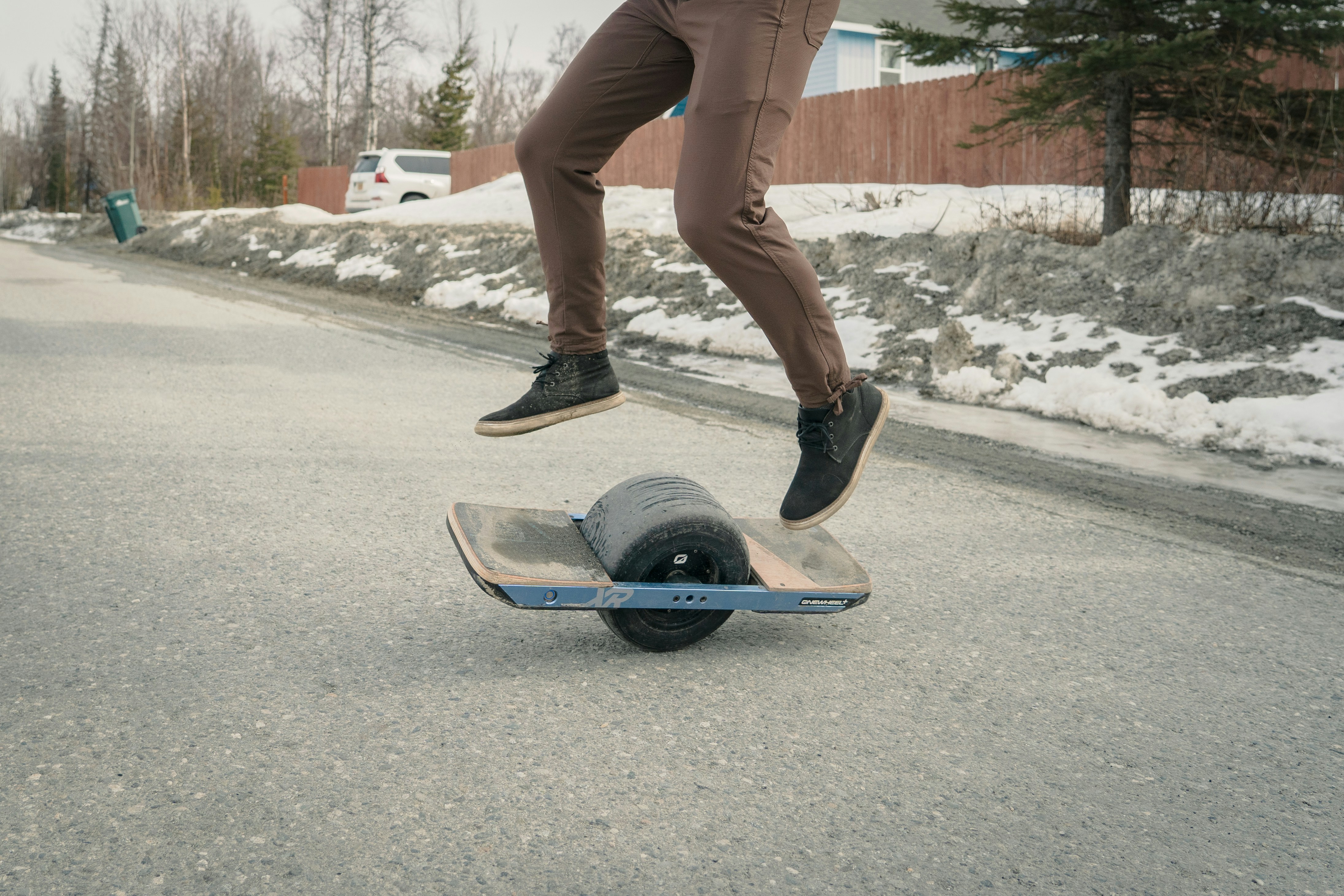 A person balances on a one-wheeled board while leaping in mid-air on a snowy street. The scene captures the thrill of urban adventure.