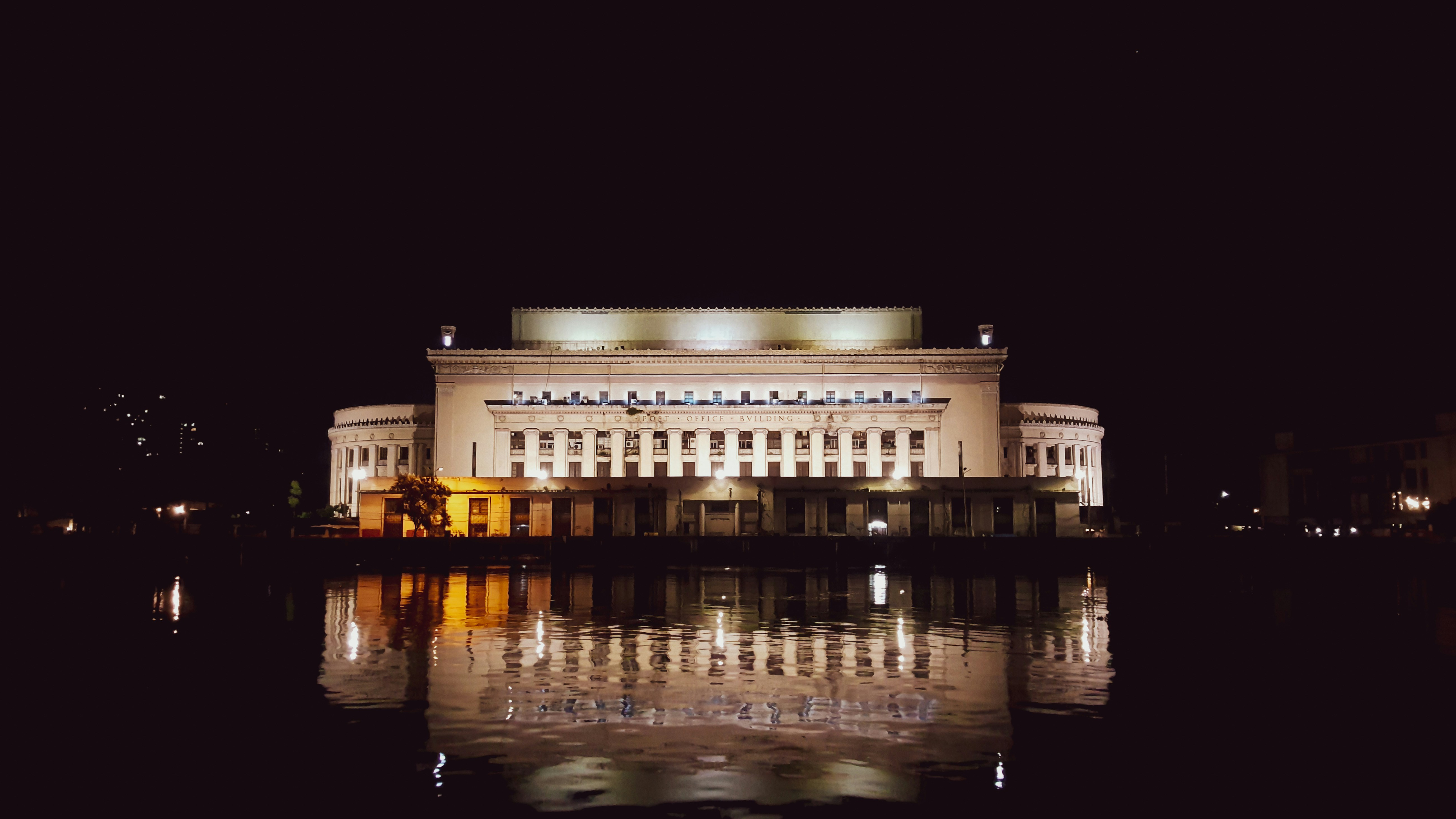 Historic Manila Post Office building lit up against the night sky with its reflection shimmering in the still water.