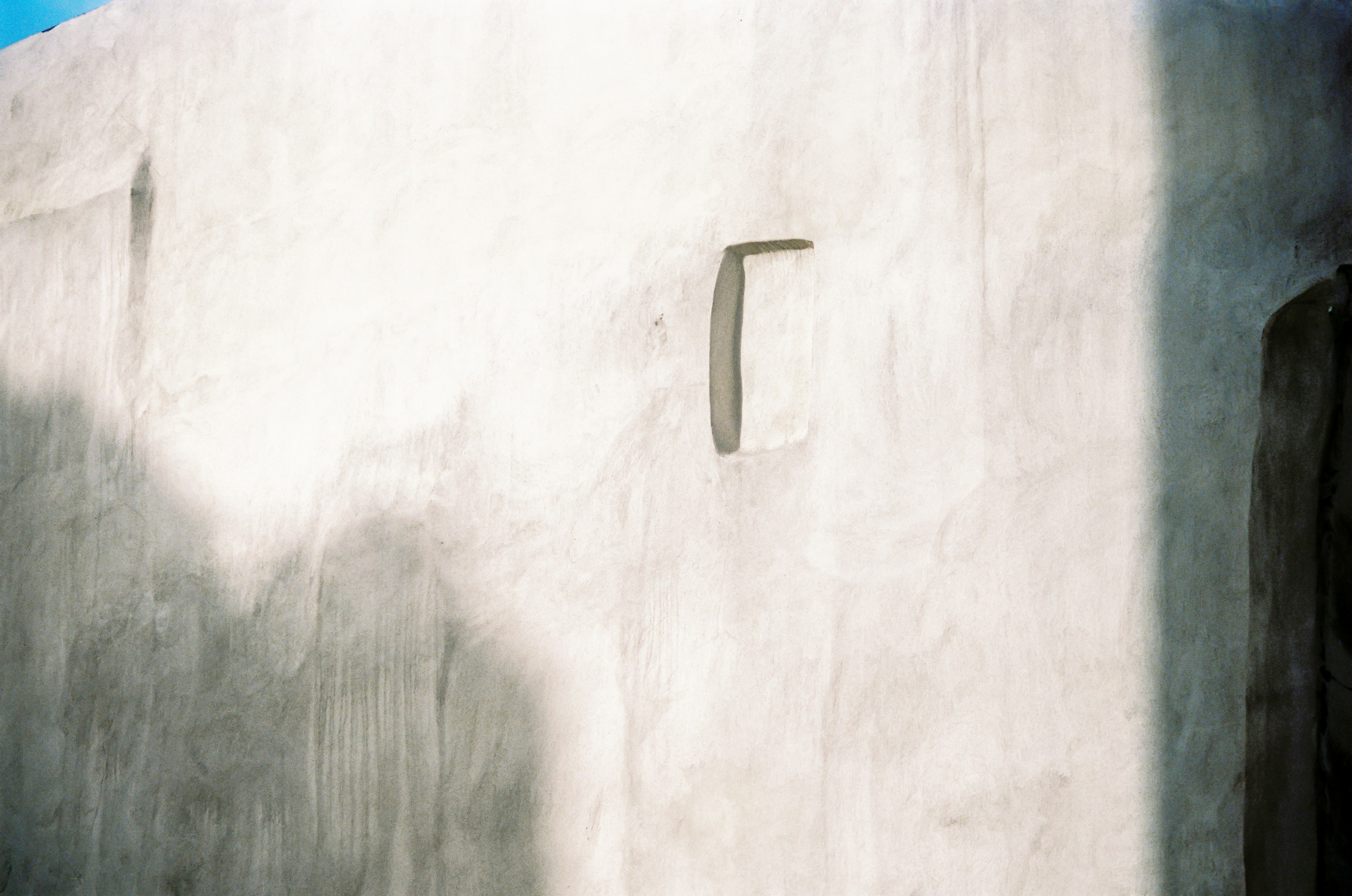 Textured wall with a subtle opening, contrasting light and shadow, showcasing the simplicity of architectural elements.