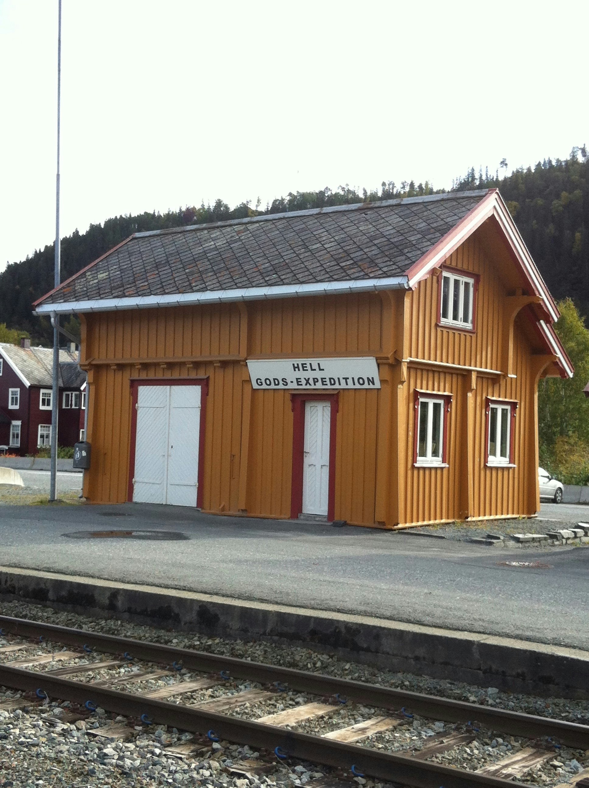 Colorful wooden building labeled 'HELL GODS-EXPEDITION' at a train station, surrounded by a picturesque landscape.