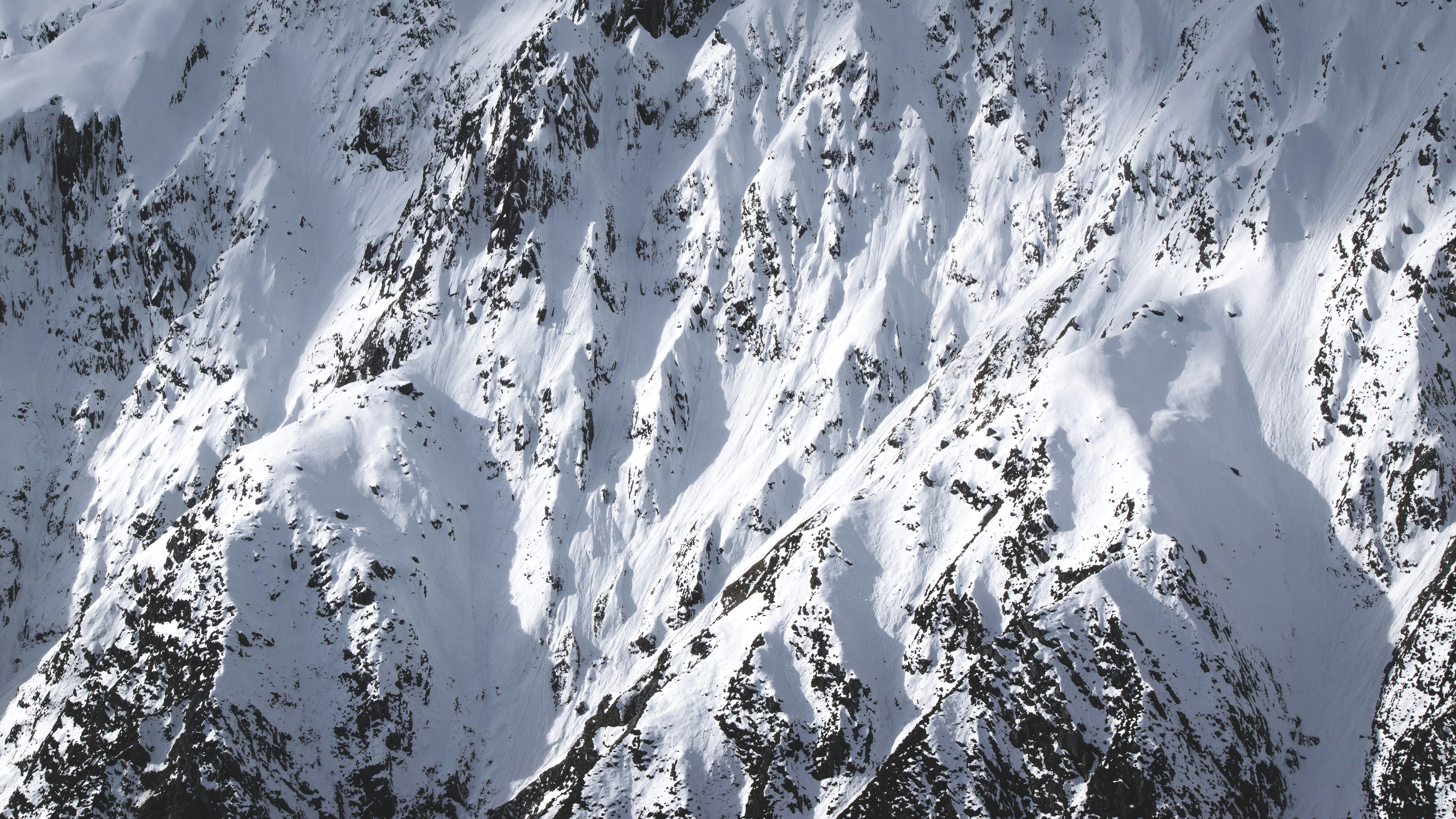 Skier navigating steep, snow-laden mountain face under bright sunlight.