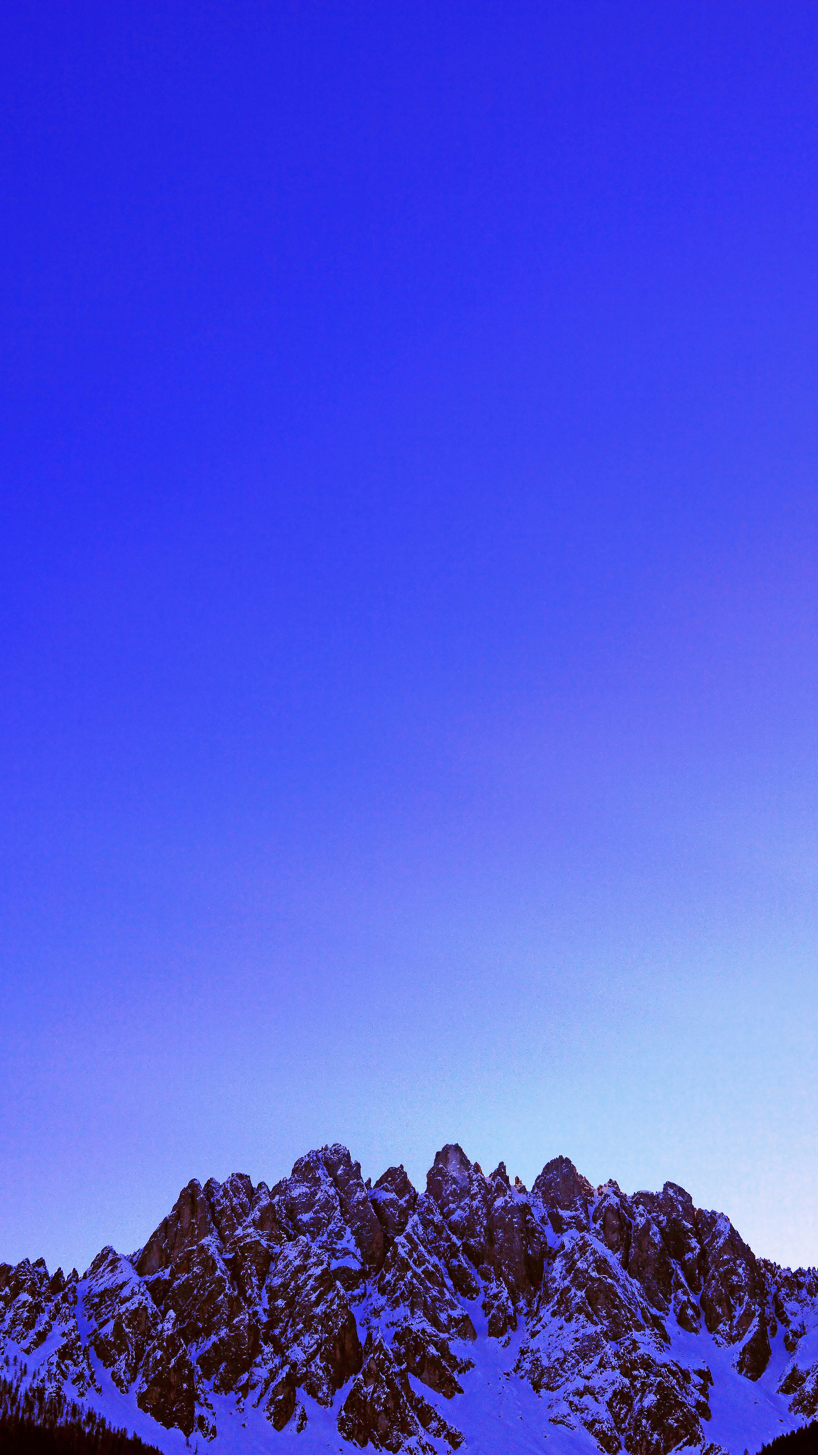 Snow-covered mountain range silhouetted against a deep blue twilight sky.