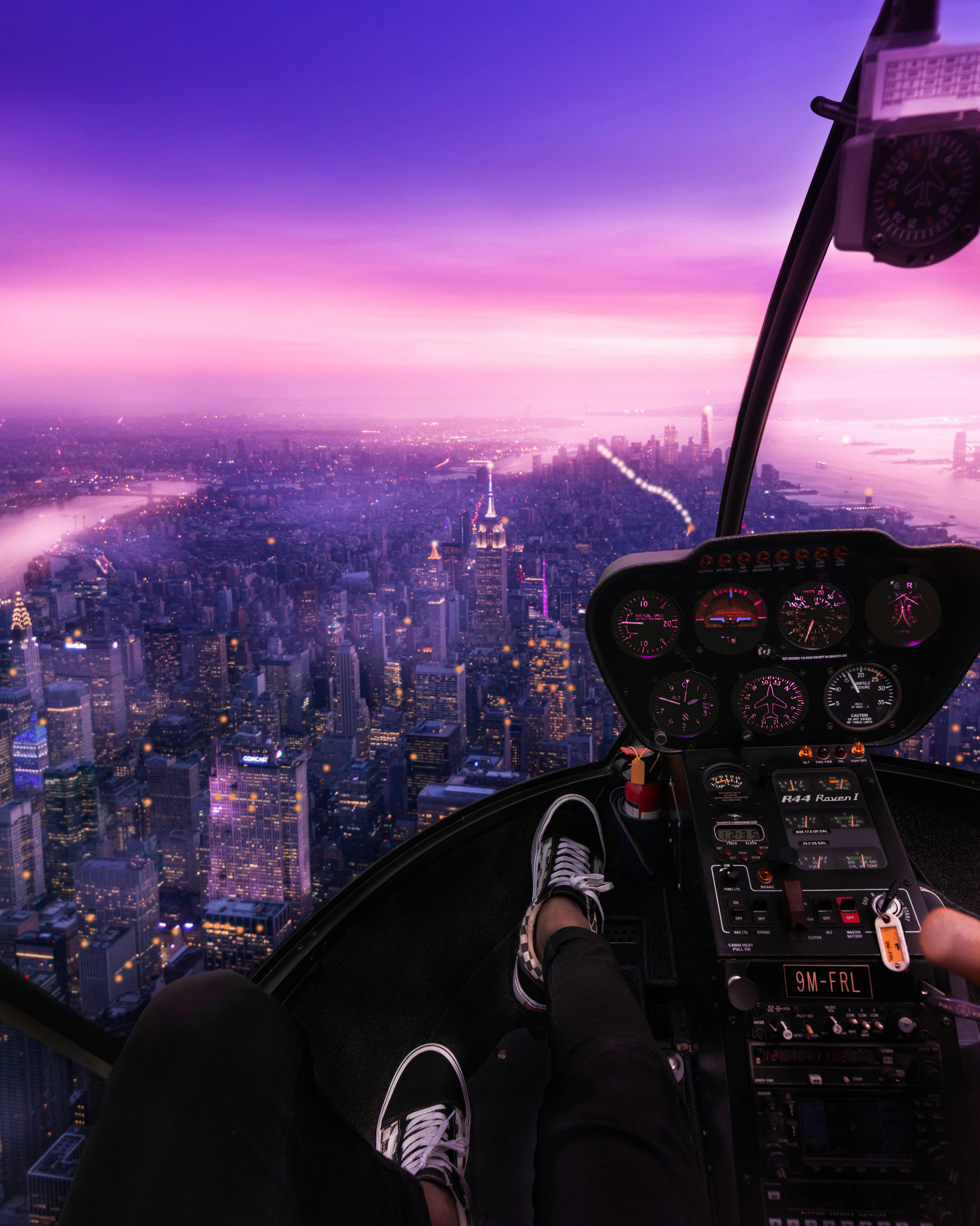 Helicopter cockpit view over a sprawling cityscape at twilight, showcasing illuminated skyscrapers and a vibrant sky. 