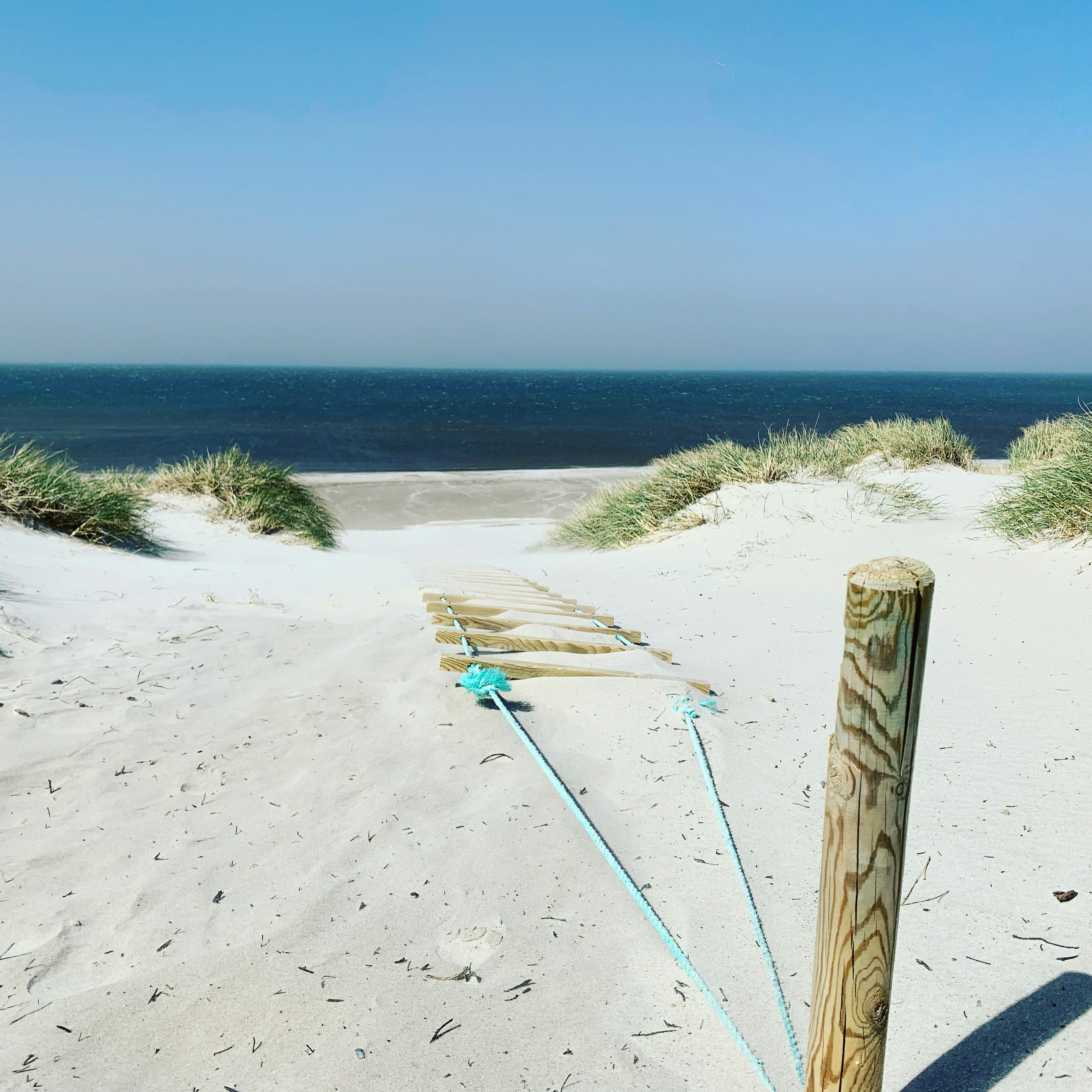 Wooden walkway leading to a tranquil beach scene with gentle waves and lush grass on either side.