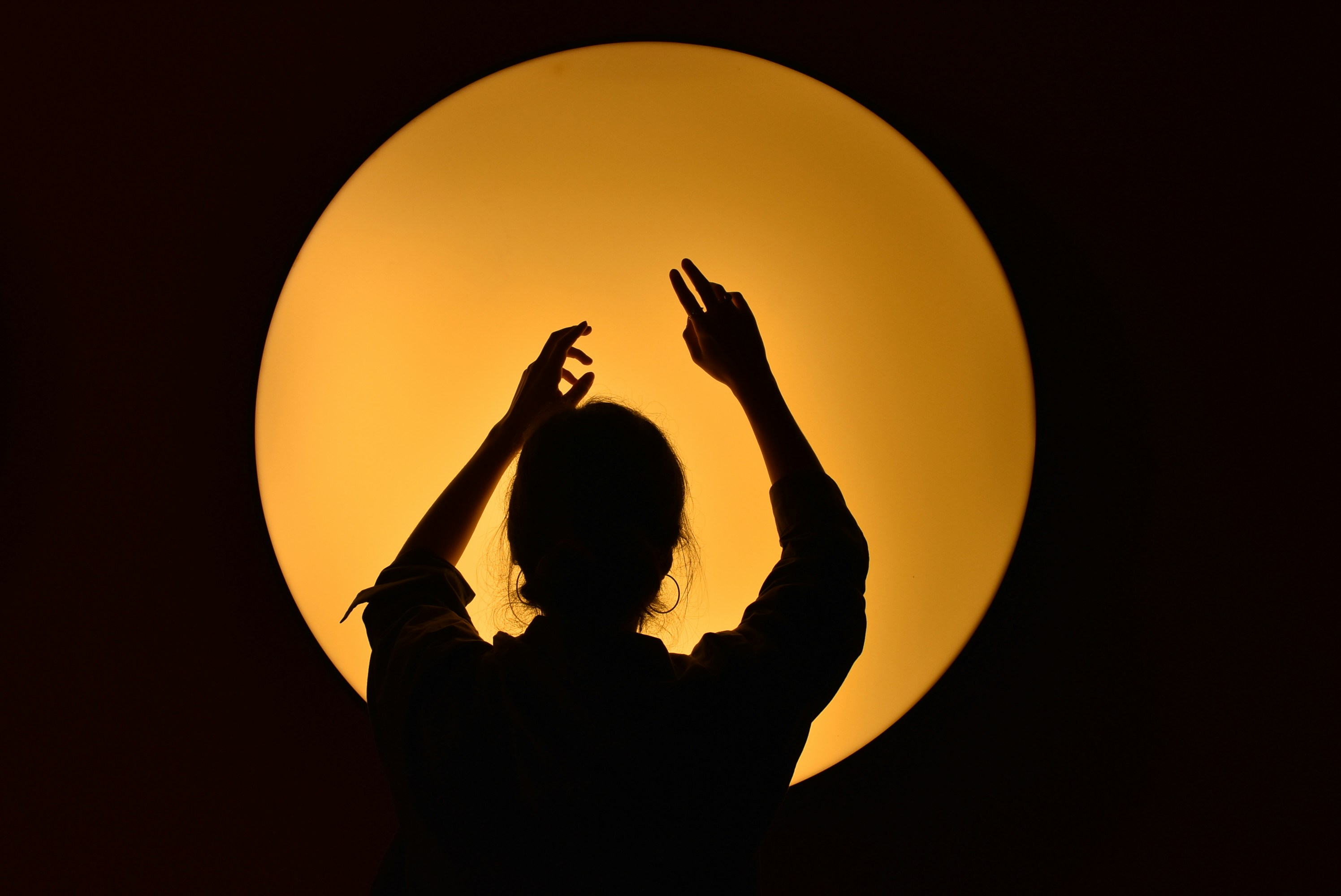 Golden Halo Silhouette: Raising Hands Before a Backlit Orb