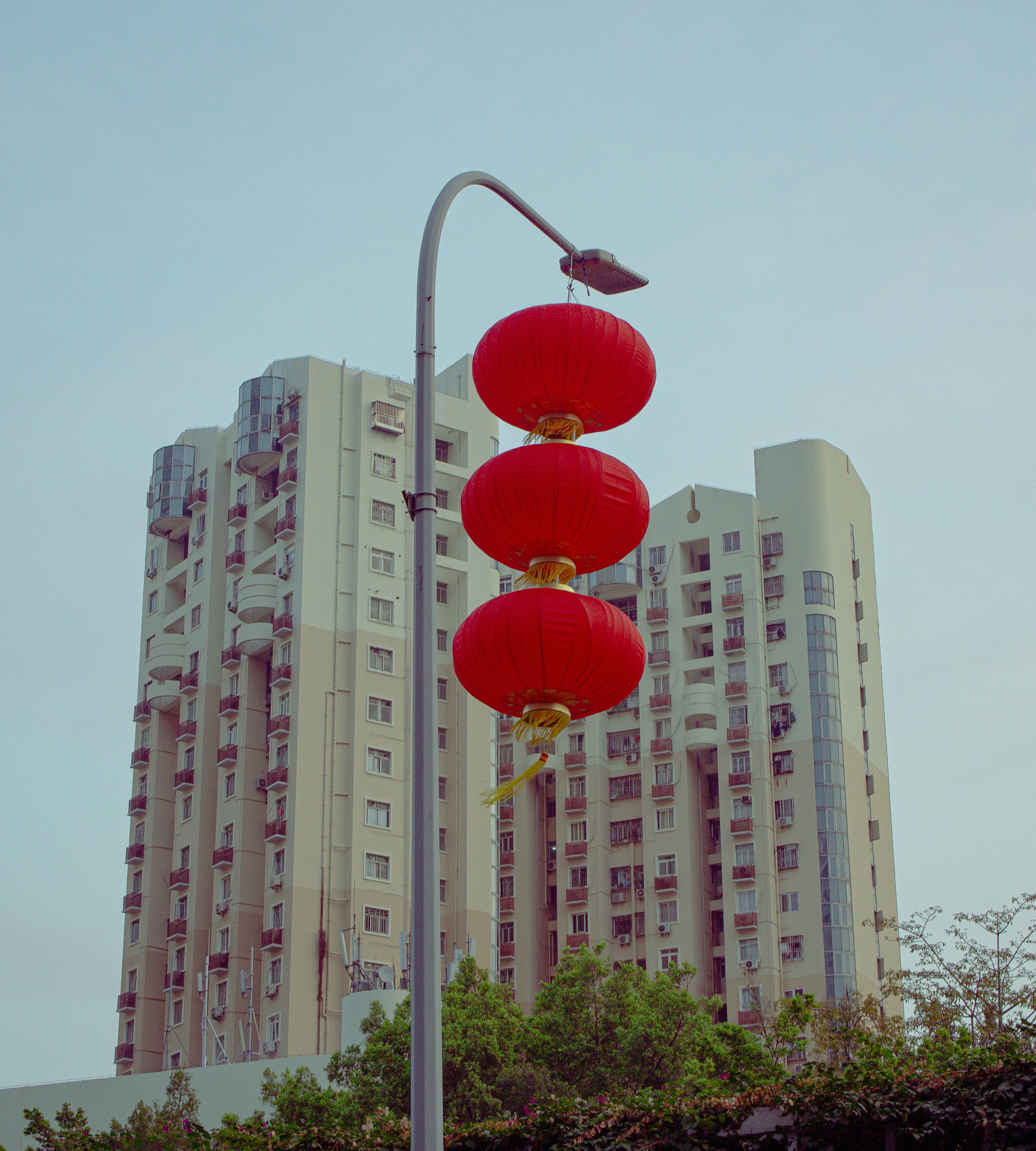 Three vibrant red lanterns hanging from a streetlight, juxtaposed against a backdrop of modern apartment buildings.