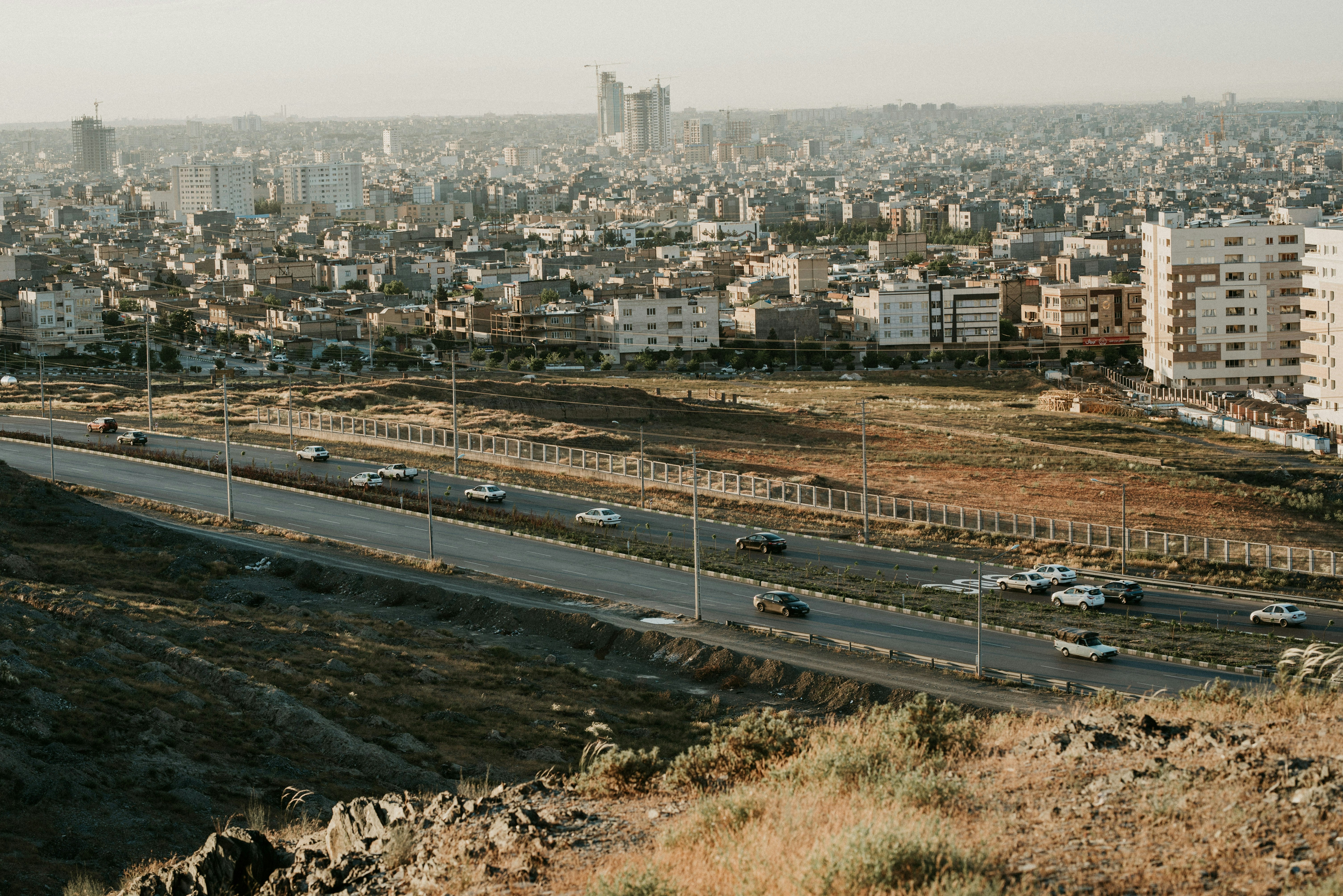 Expansive cityscape view of Mashhad from an elevated vantage point, with a highway cutting through the foreground.