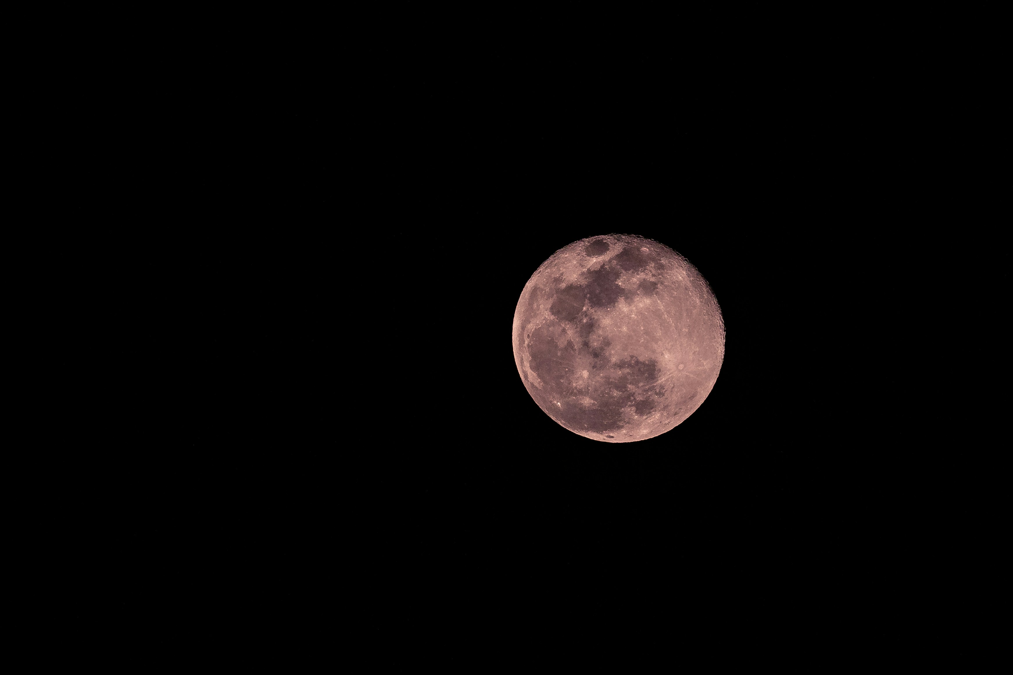 Full moon with a subtle pink hue against a dark night sky.