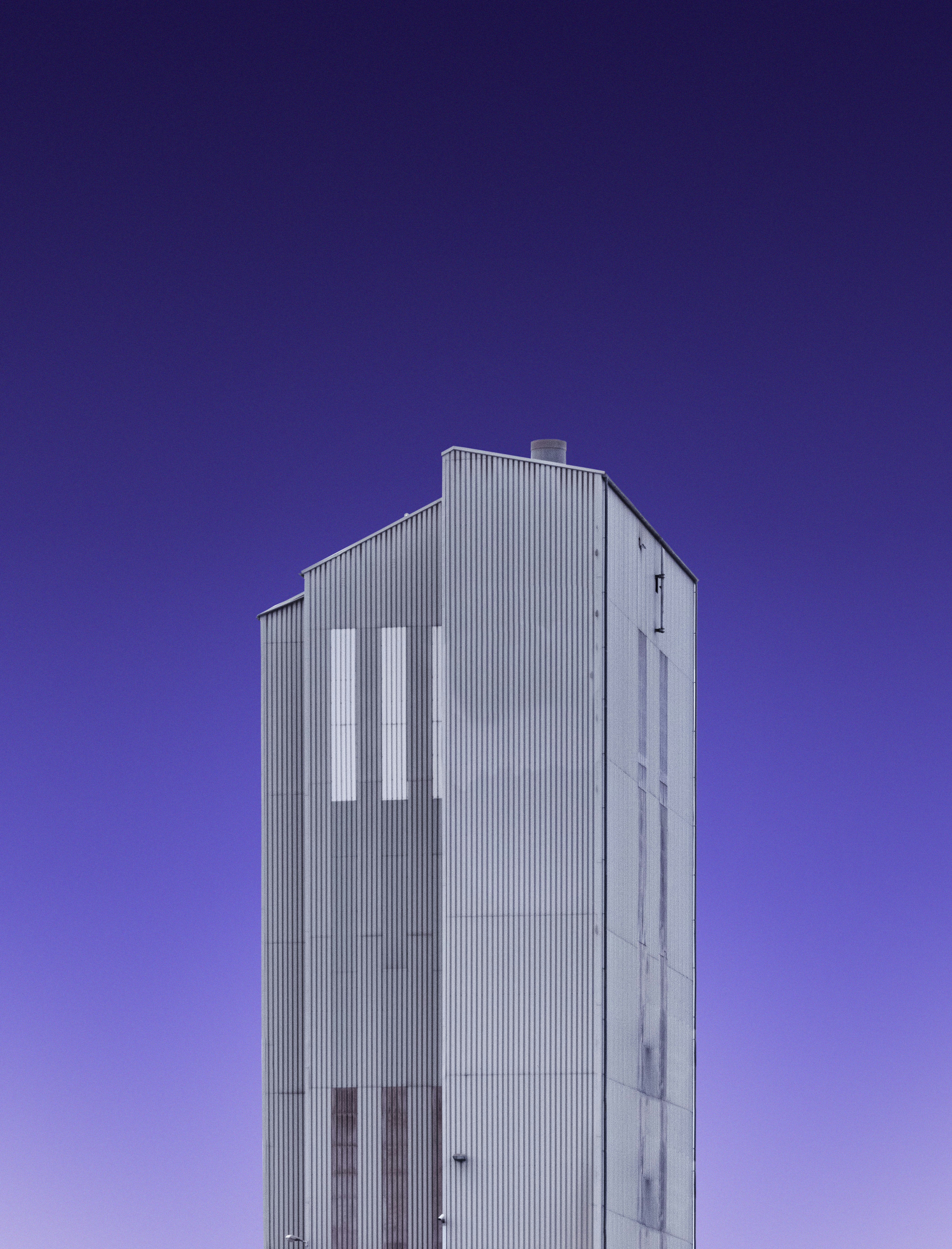 A tall, industrial building with a corrugated exterior stands against a deep purple sky, evoking a sense of isolation and modernity.