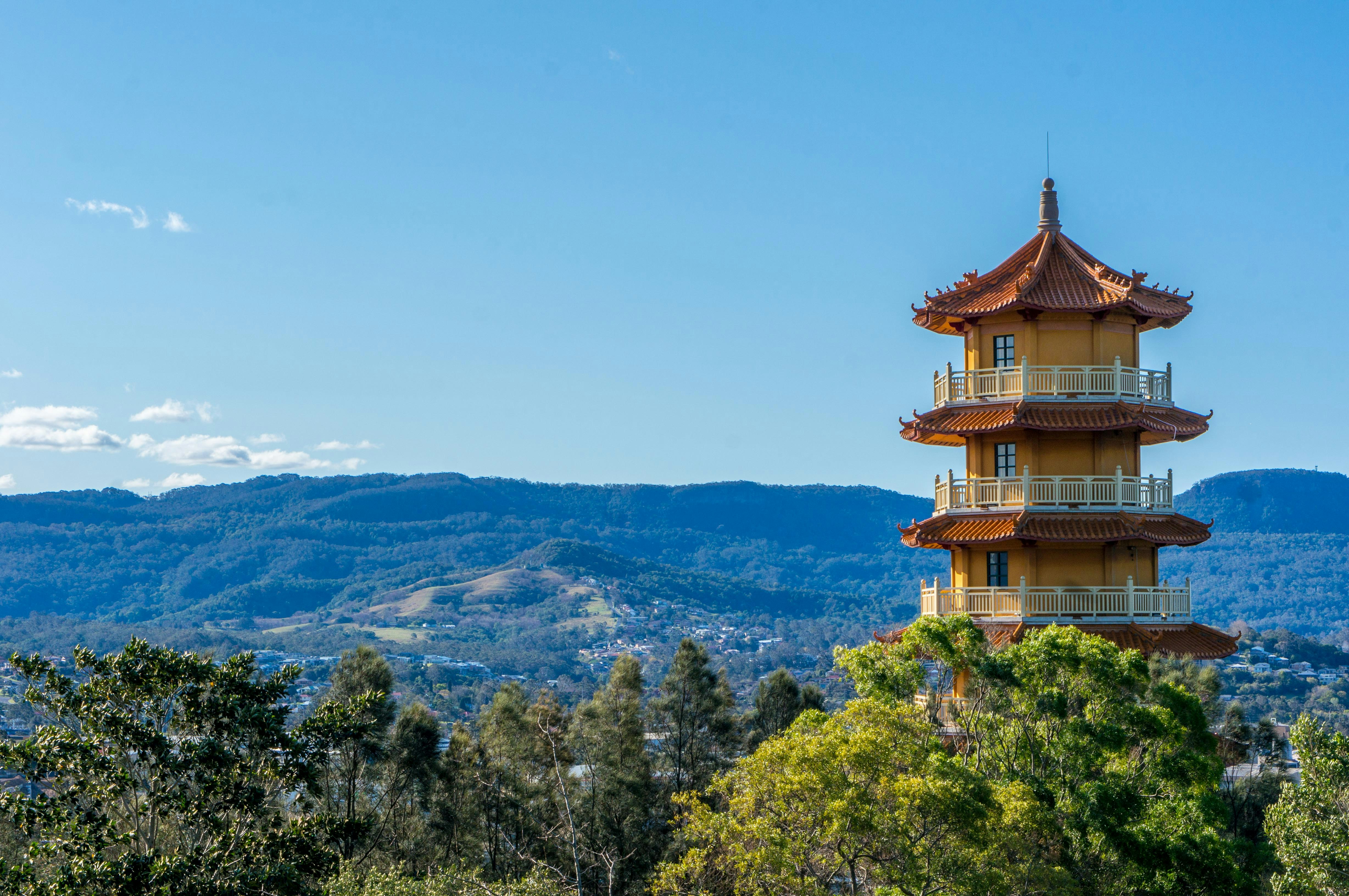Traditional pagoda rising above lush greenery with distant blue mountains under a clear sky.