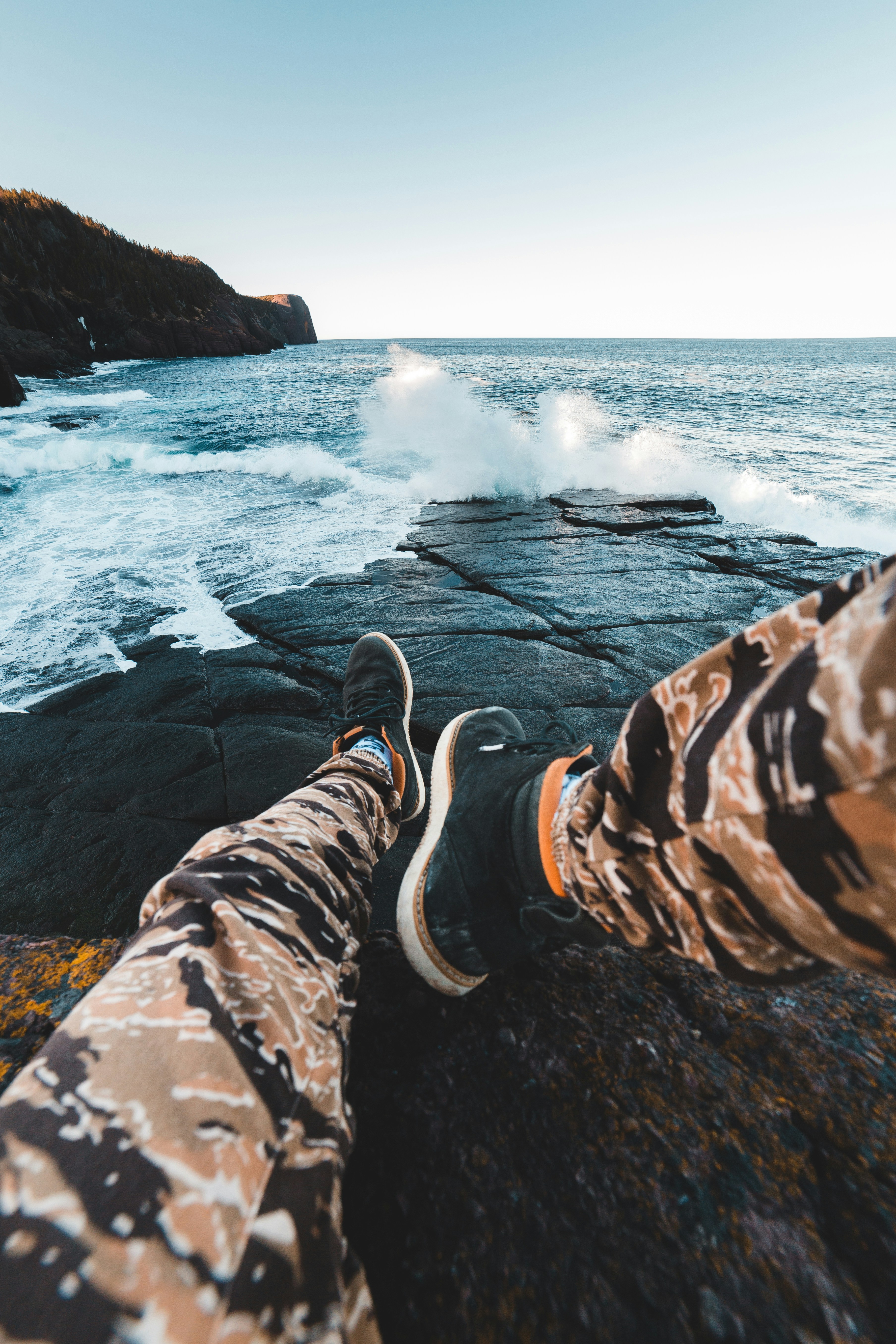 On the Edge: Sneakers Dangling Over Basalt as Sea Spray Explodes