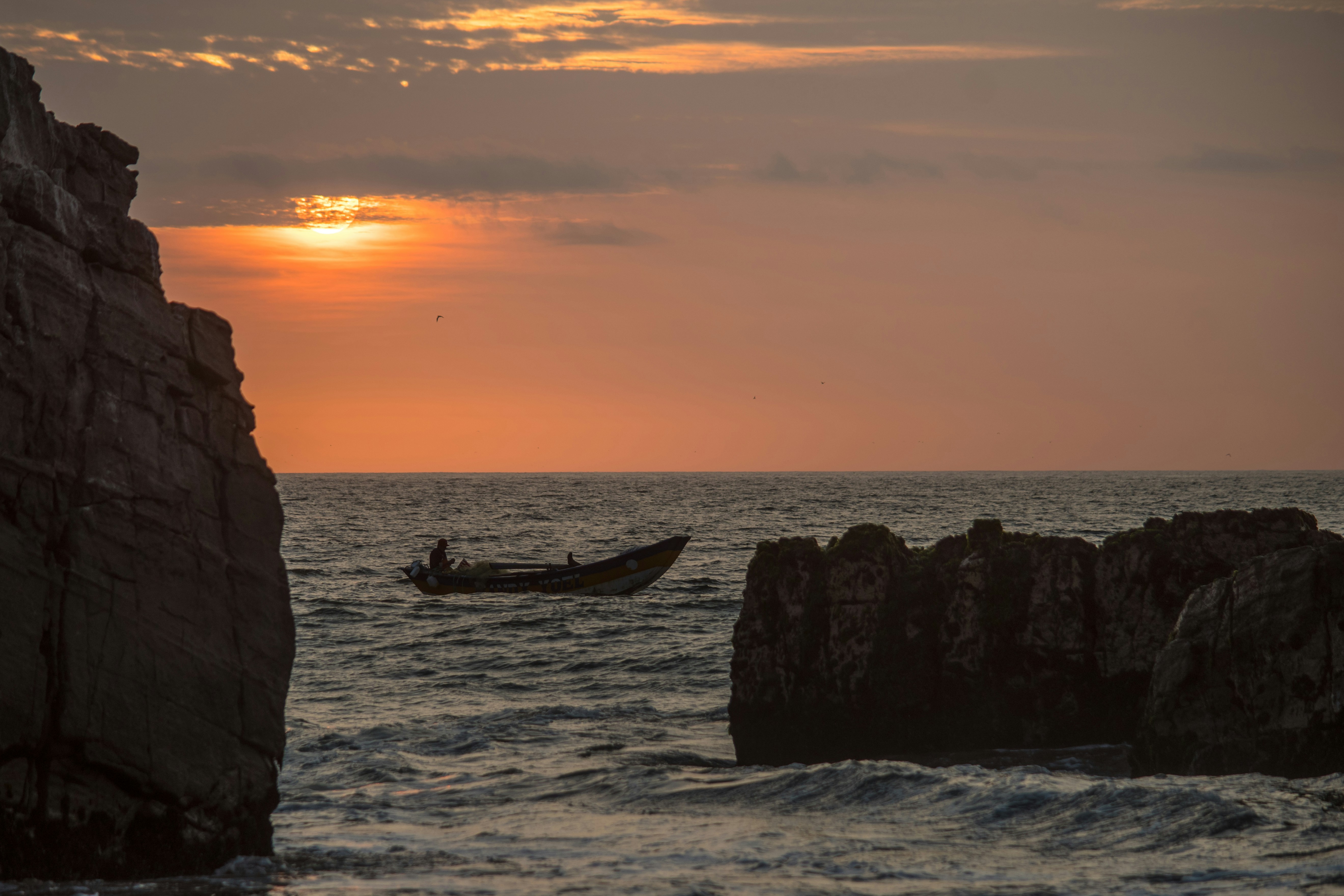 Dusk Between Sentinels: A lone boat on orange-tinted seas