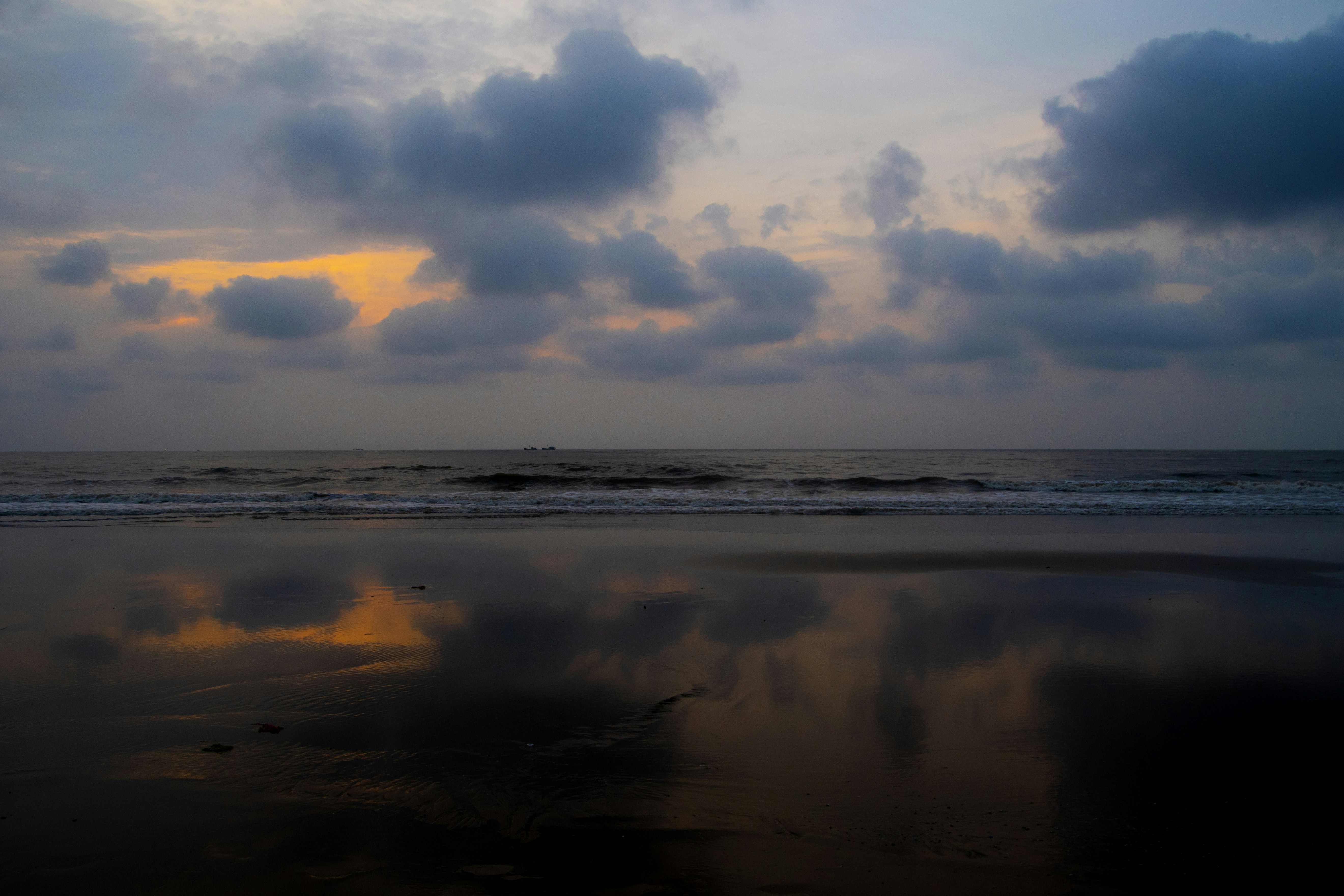 Clouds reflecting on calm ocean waters at sunrise.