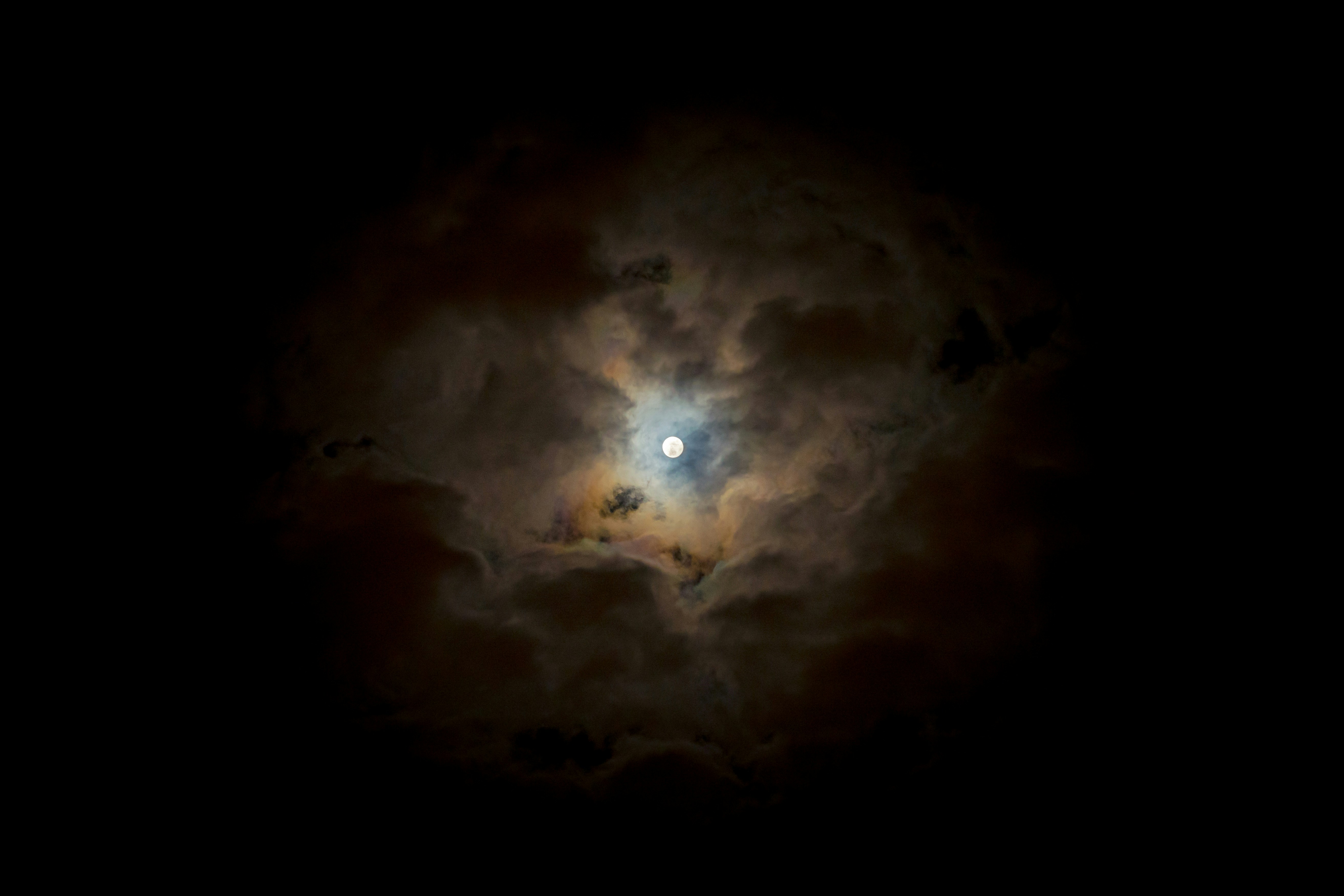 Full moon peeking through swirling dark clouds, creating a halo effect.